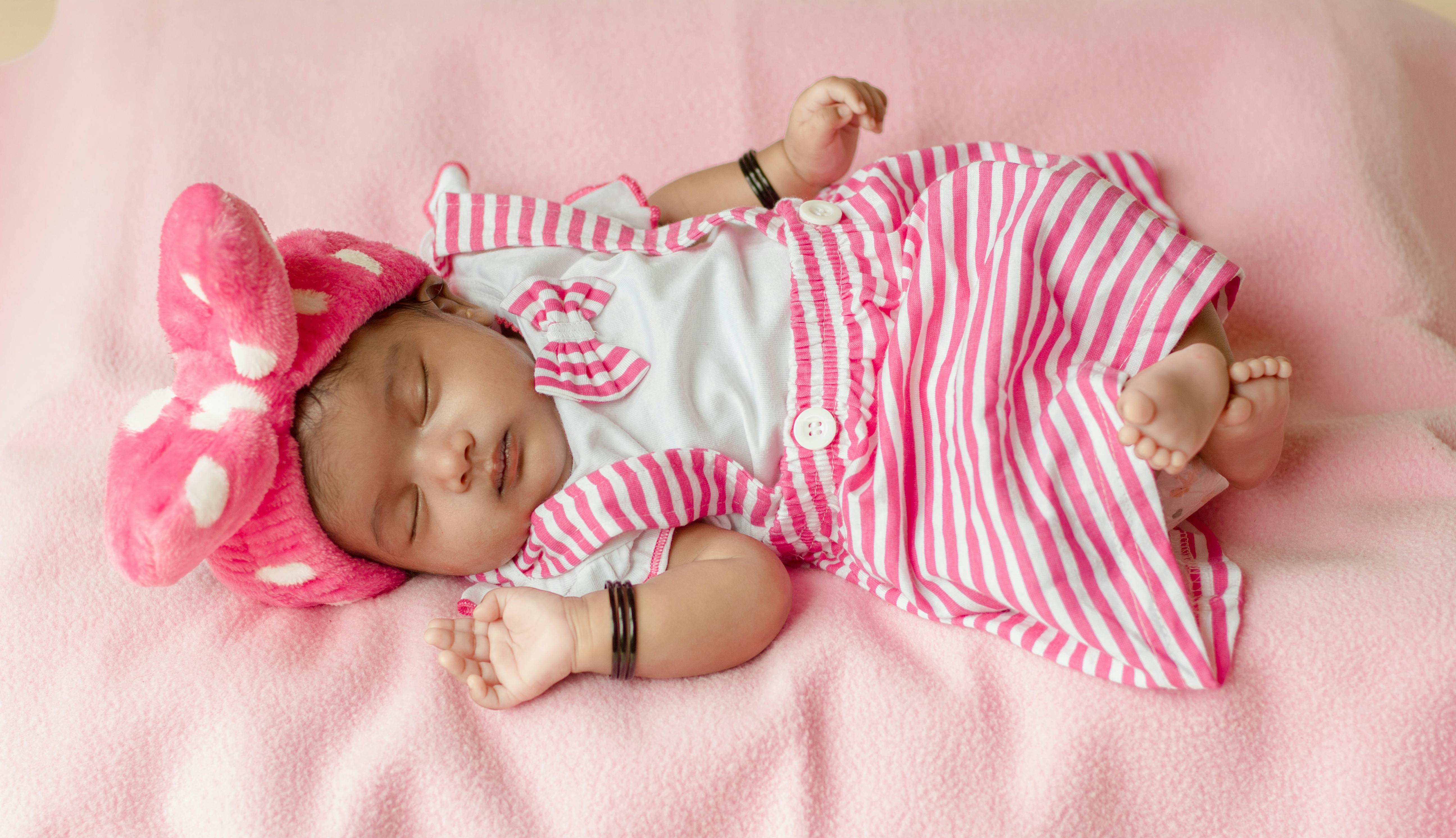 A Cute Baby Girl in Pink Dress and Headband Sleeping on Pink Fabric ...