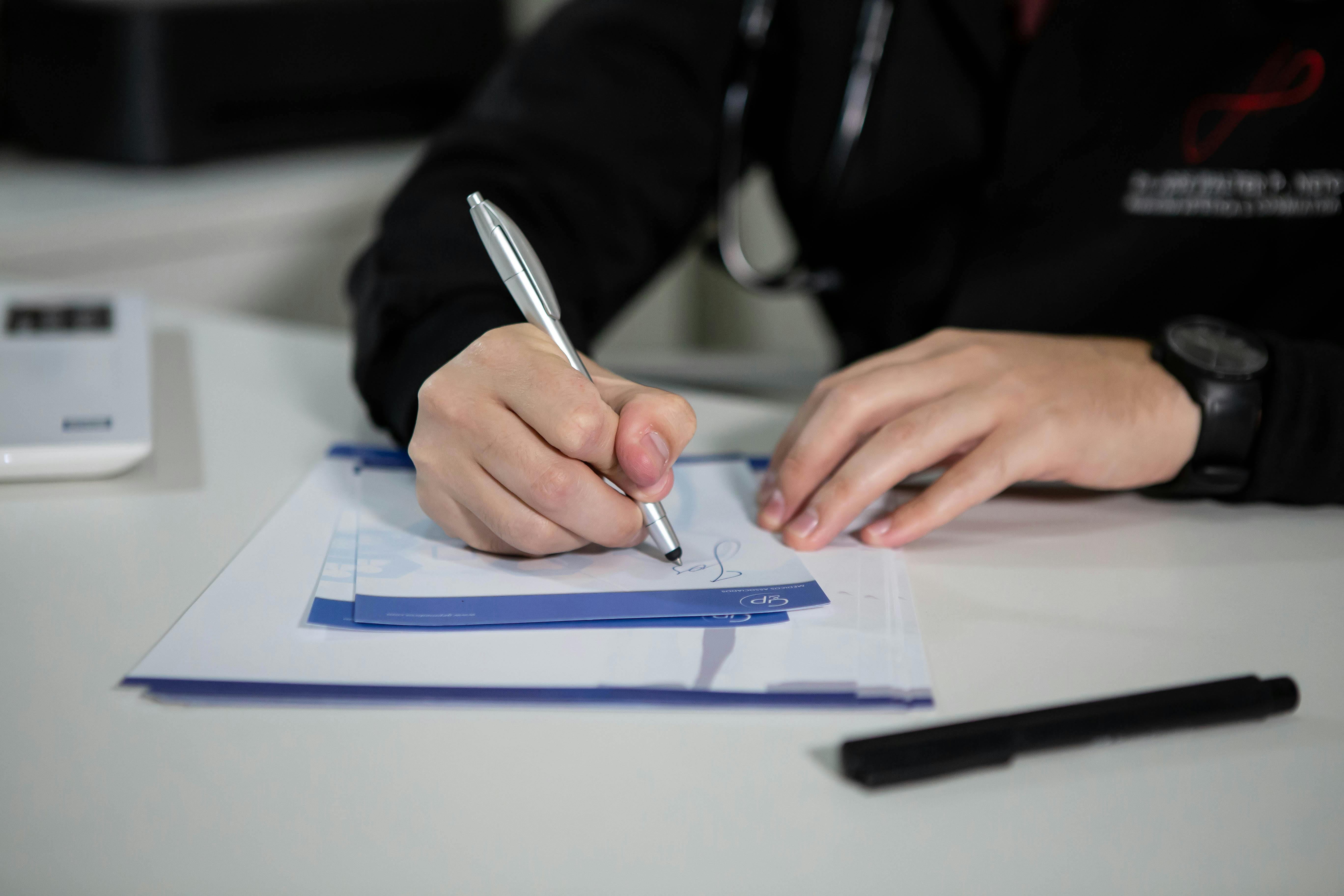 Person Holding Pen Writing on Paper · Free Stock Photo