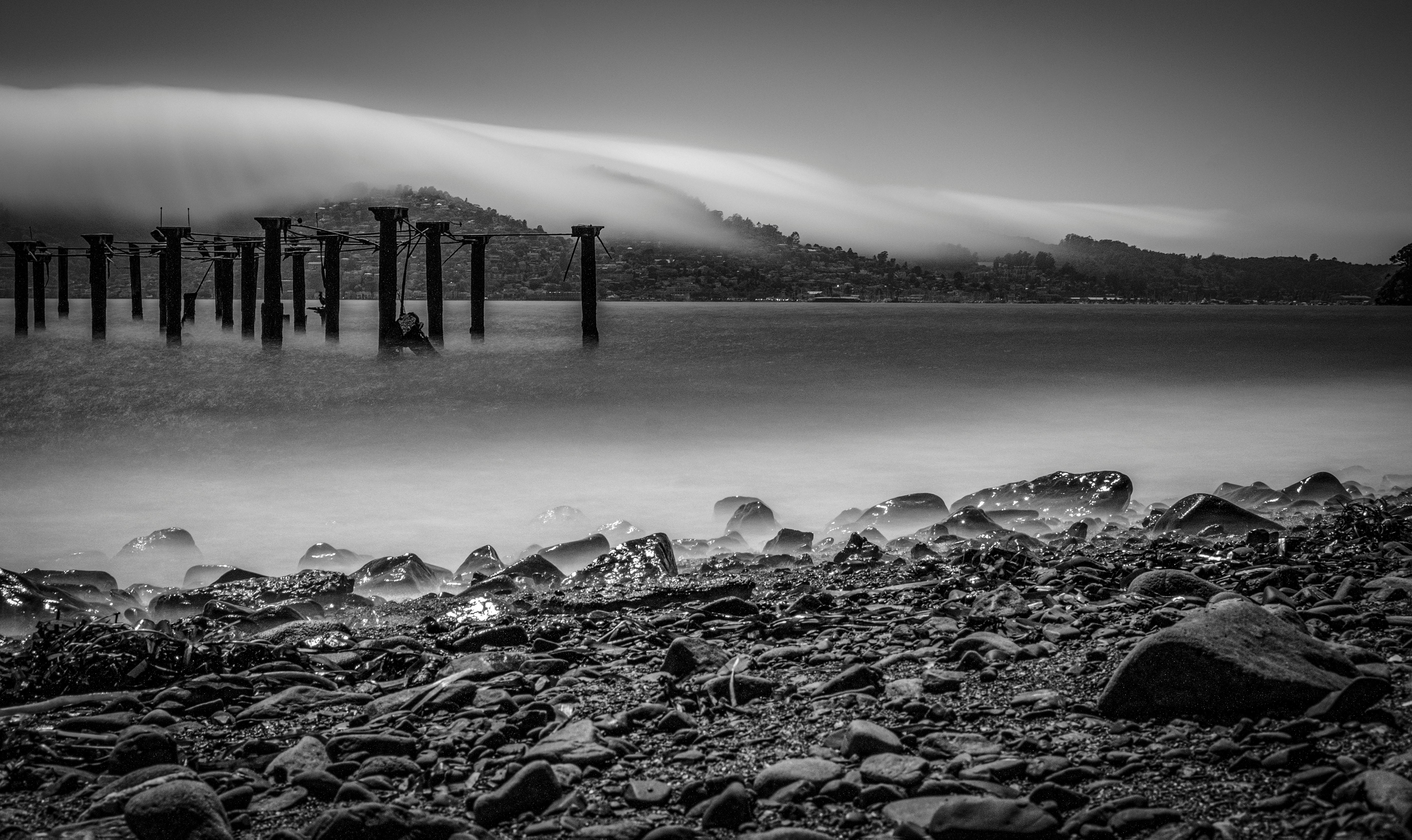 Rocks on Sea Near Mountain in Grayscale Photography · Free Stock Photo