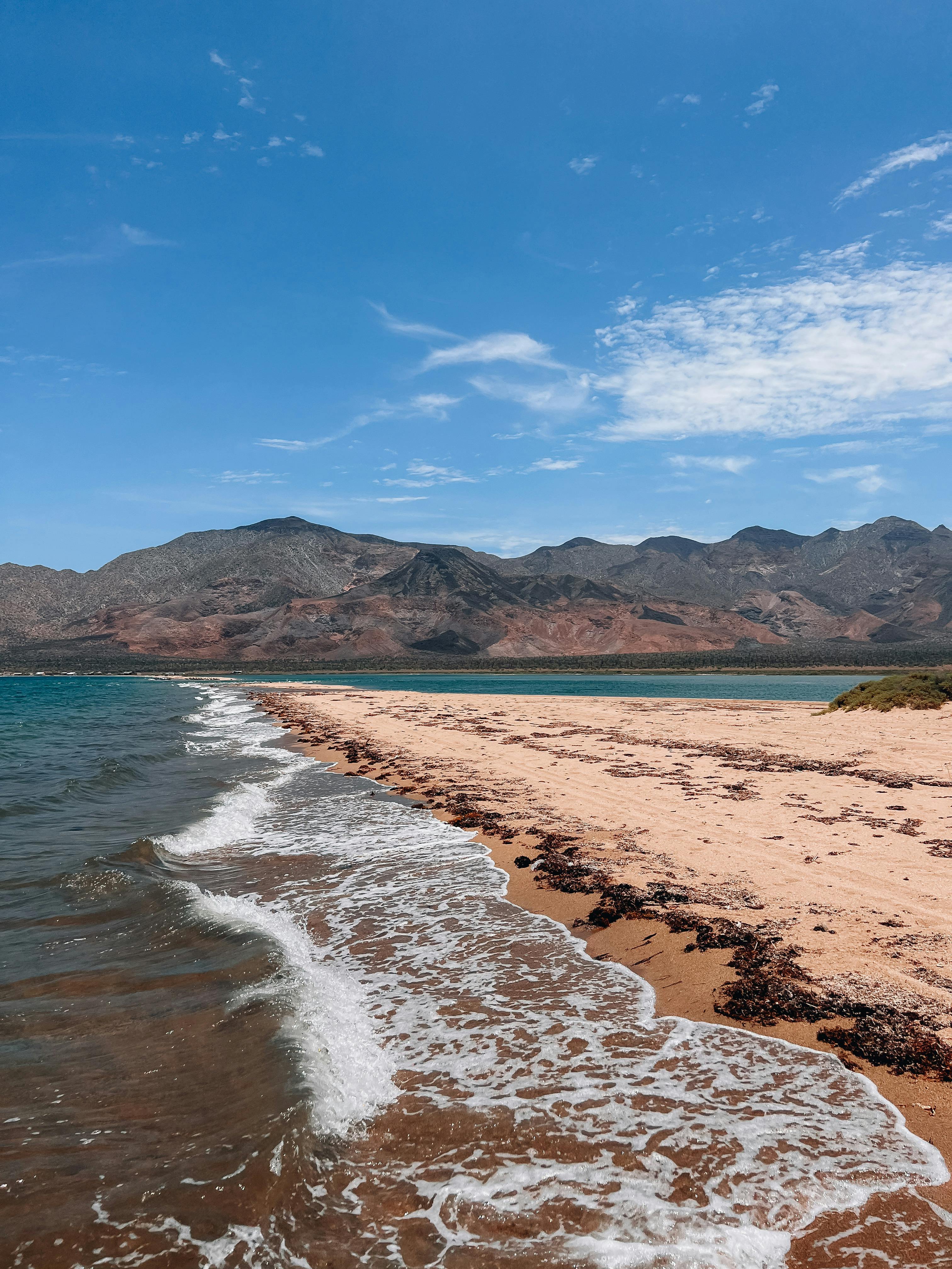 Seashore Near Mountains Under Blue Sky · Free Stock Photo