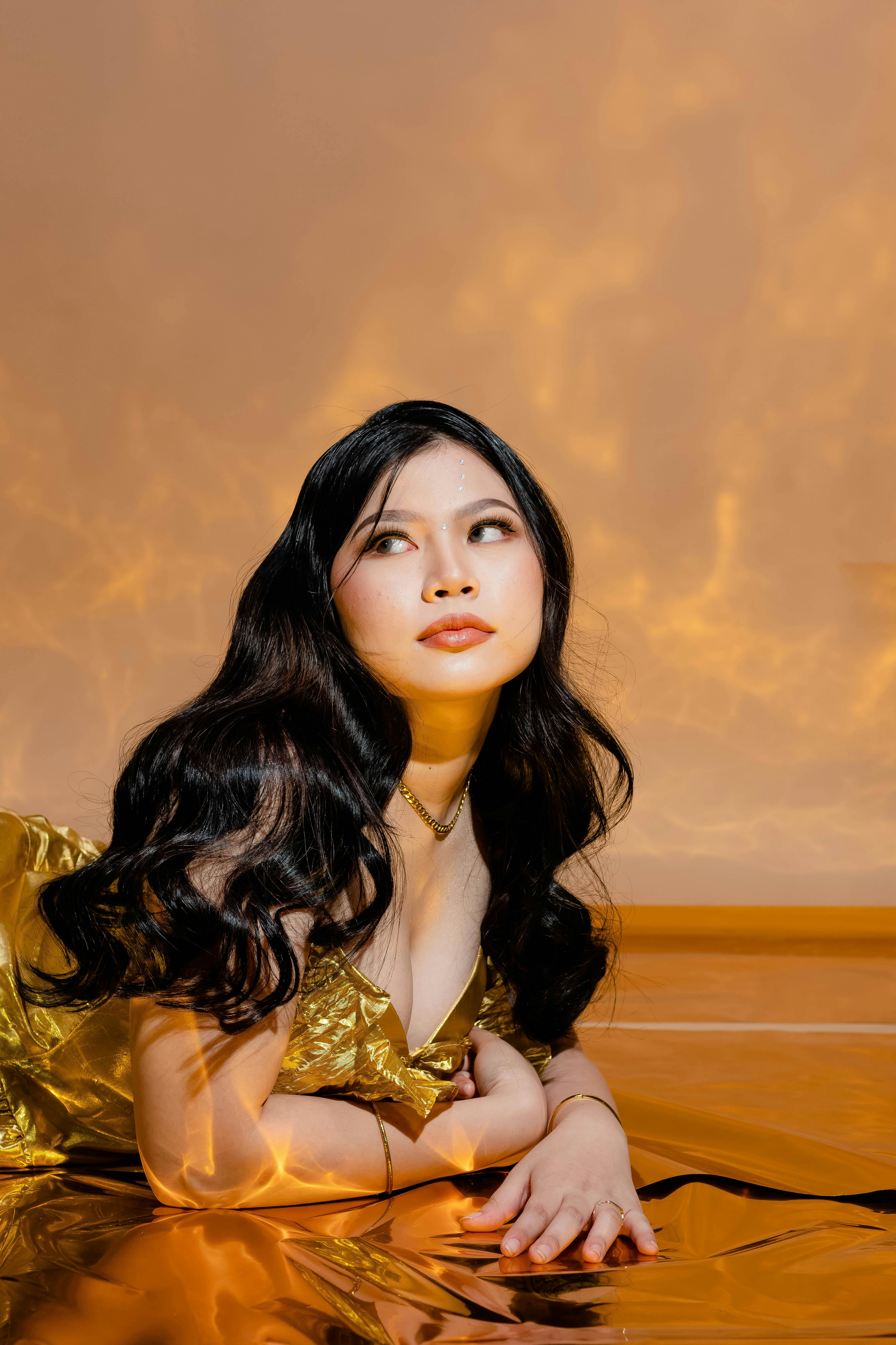 Beautiful Woman with Long Hair Lying Down on Gold Surface · Free Stock Photo