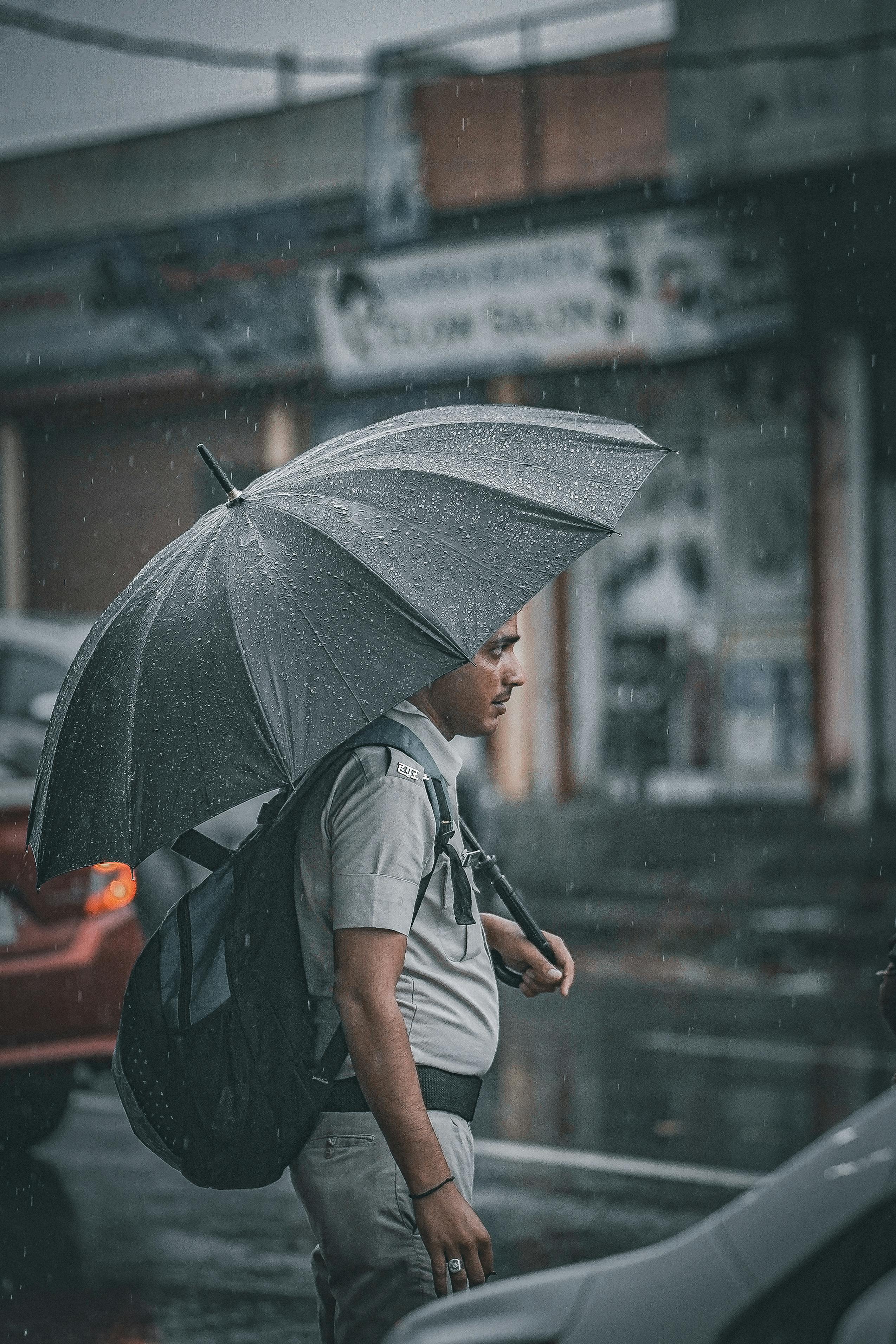 A Man in a Uniform Using an Umbrella while Raining · Free Stock Photo