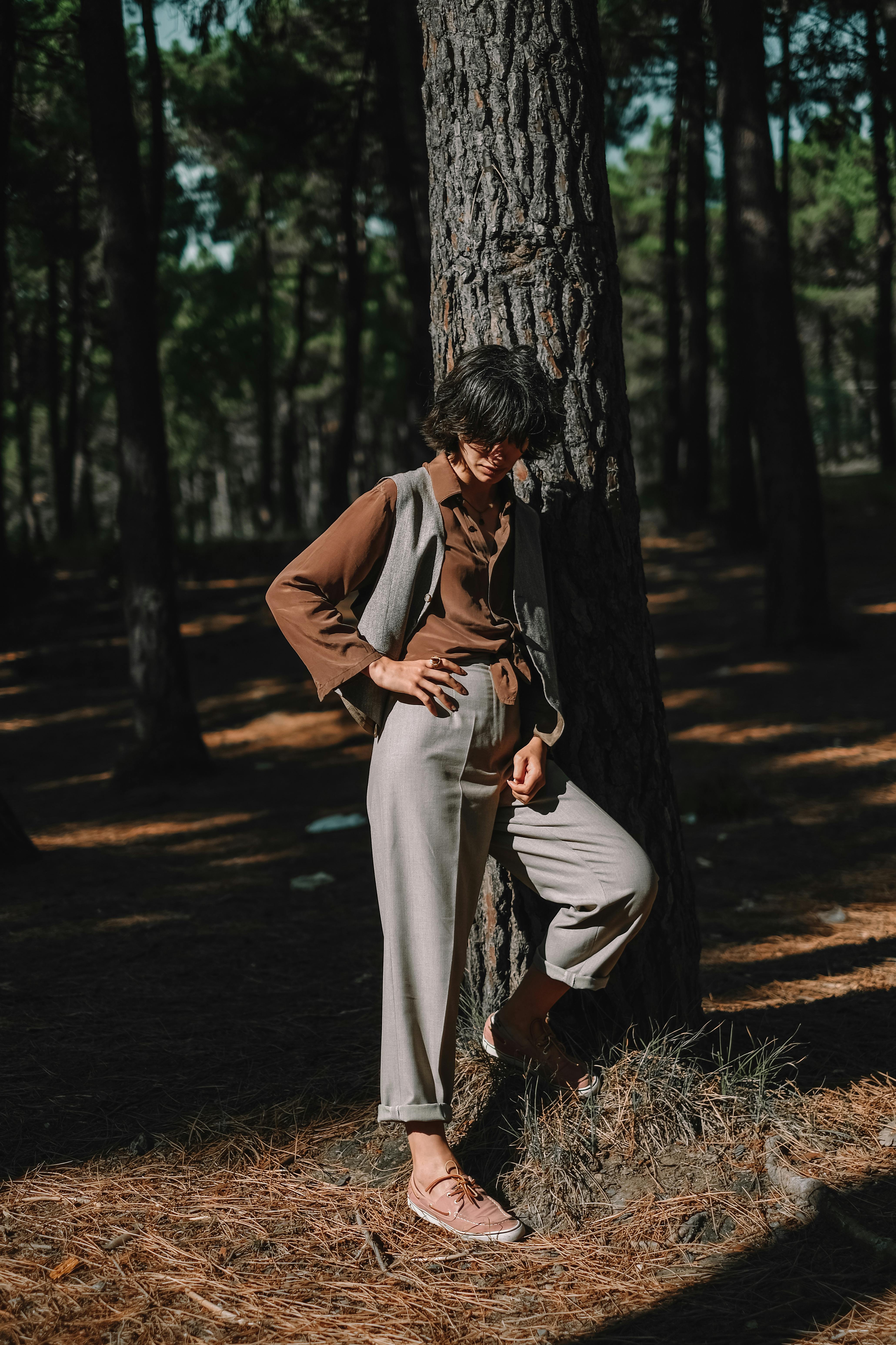 Woman Looking Down While Standing Beside Tree Trunk · Free Stock Photo