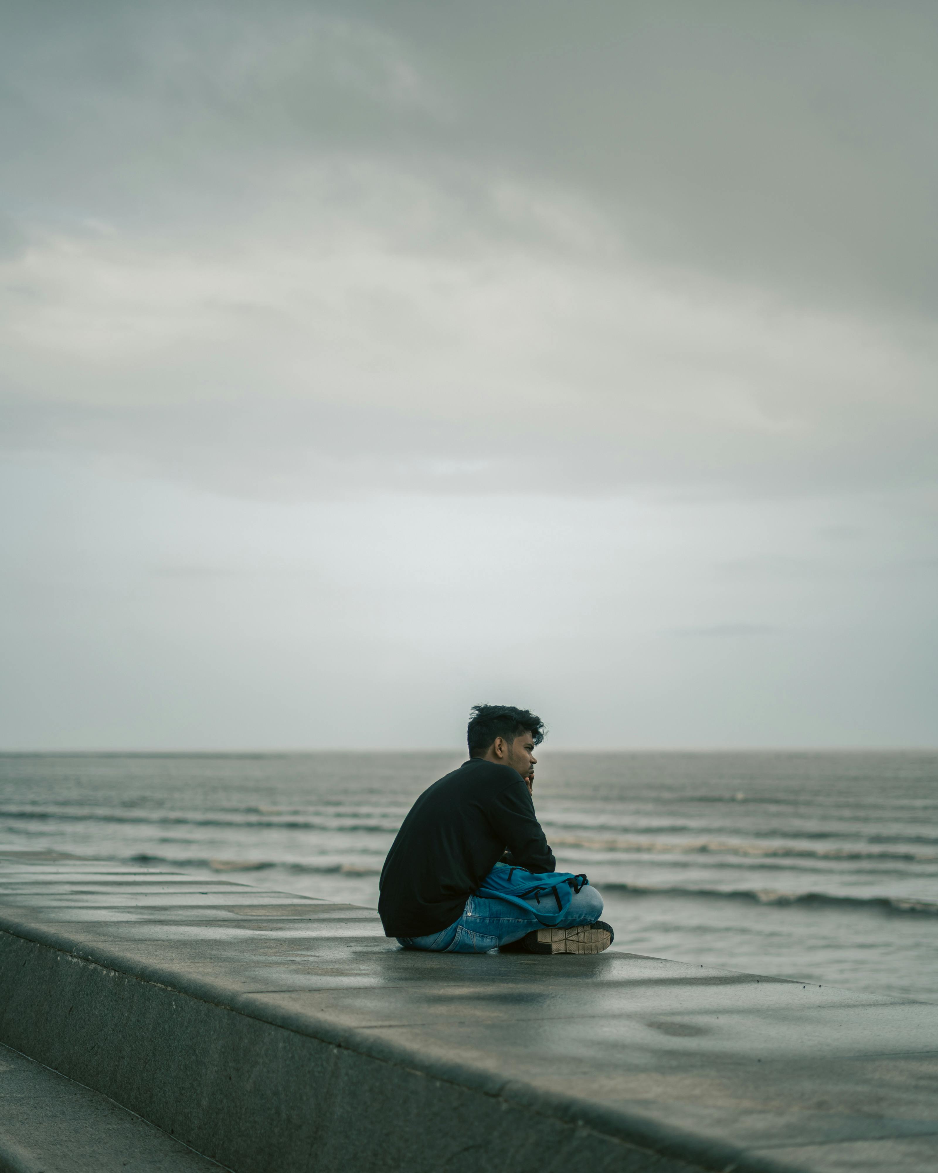 Photo of a Man Sitting Near the Sea · Free Stock Photo
