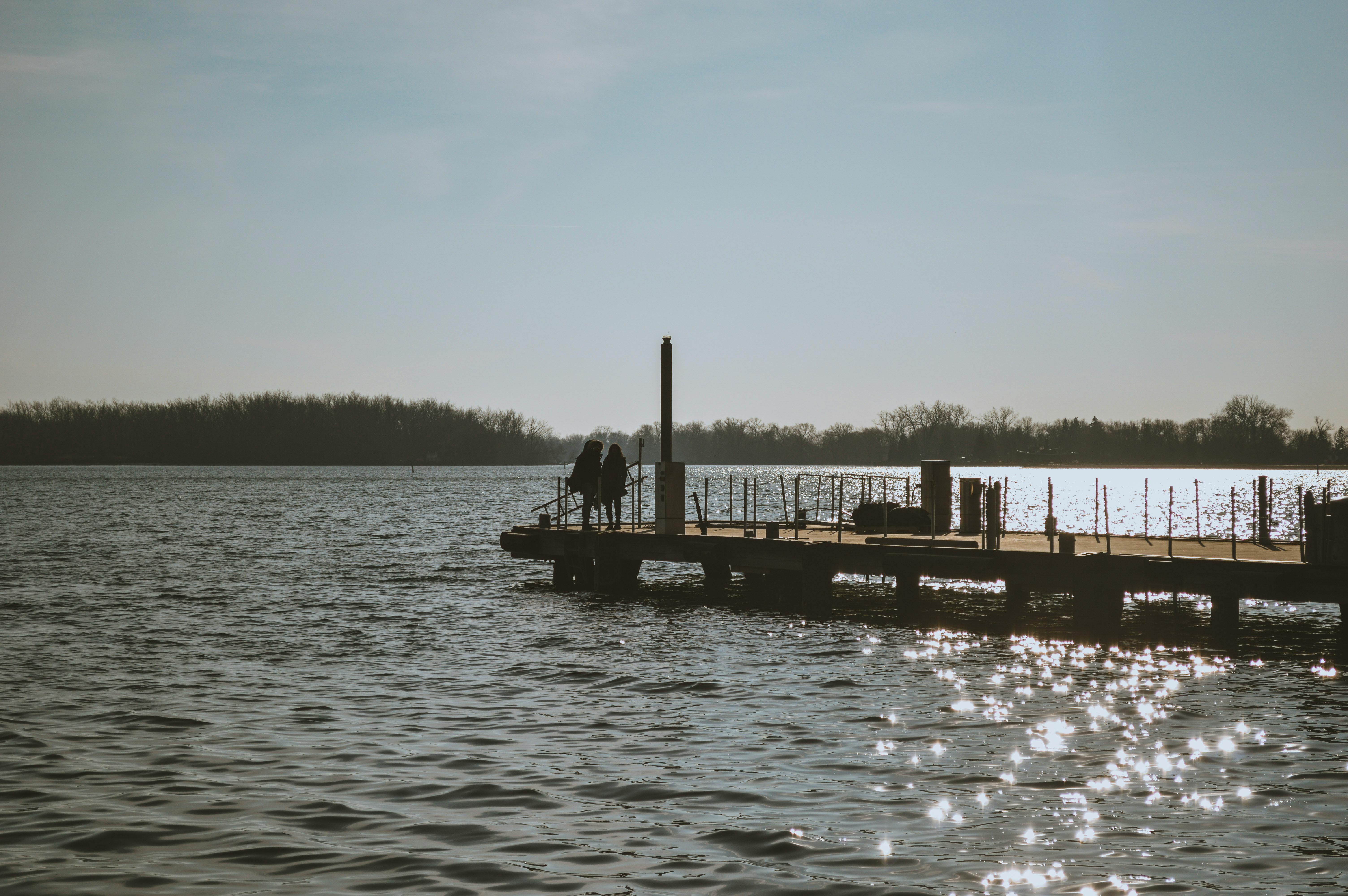 Couple Standing on Pier on Sunlit Lake · Free Stock Photo
