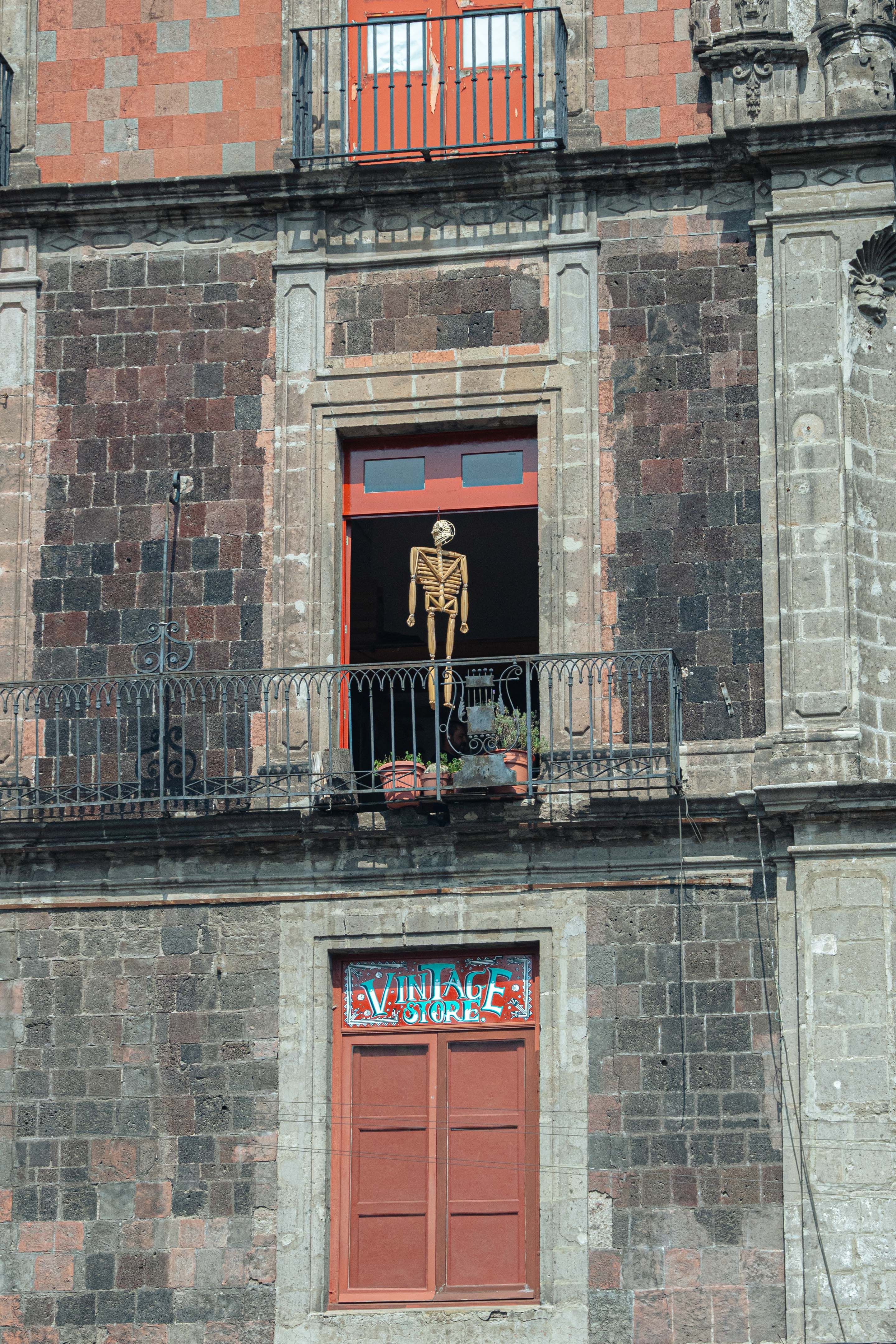 Skeleton Hanging on a Doorway of Brick Building Balcony · Free Stock Photo