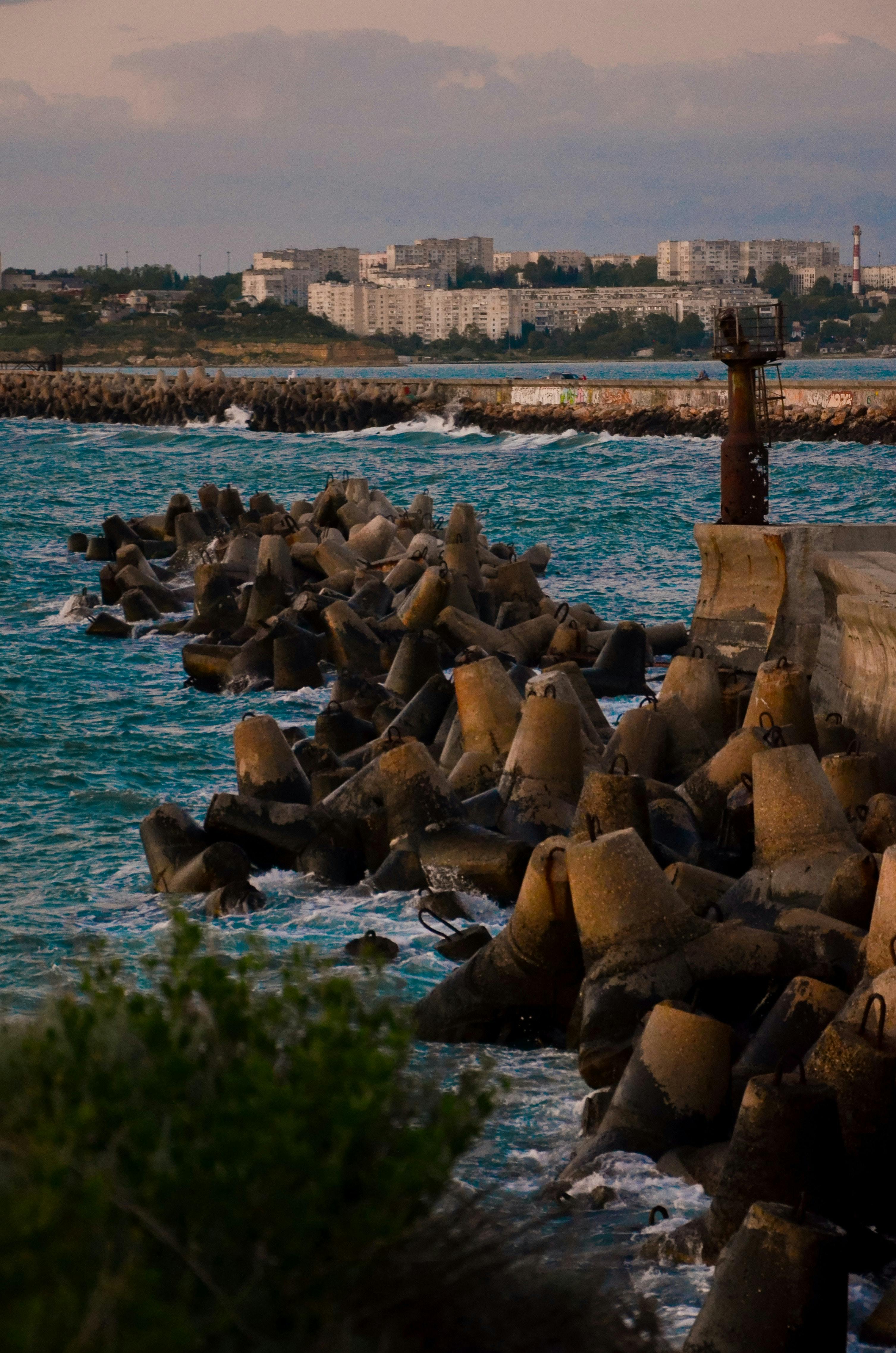 View of a Breakwater on a Shore and Buildings in Distance at Sunset ...