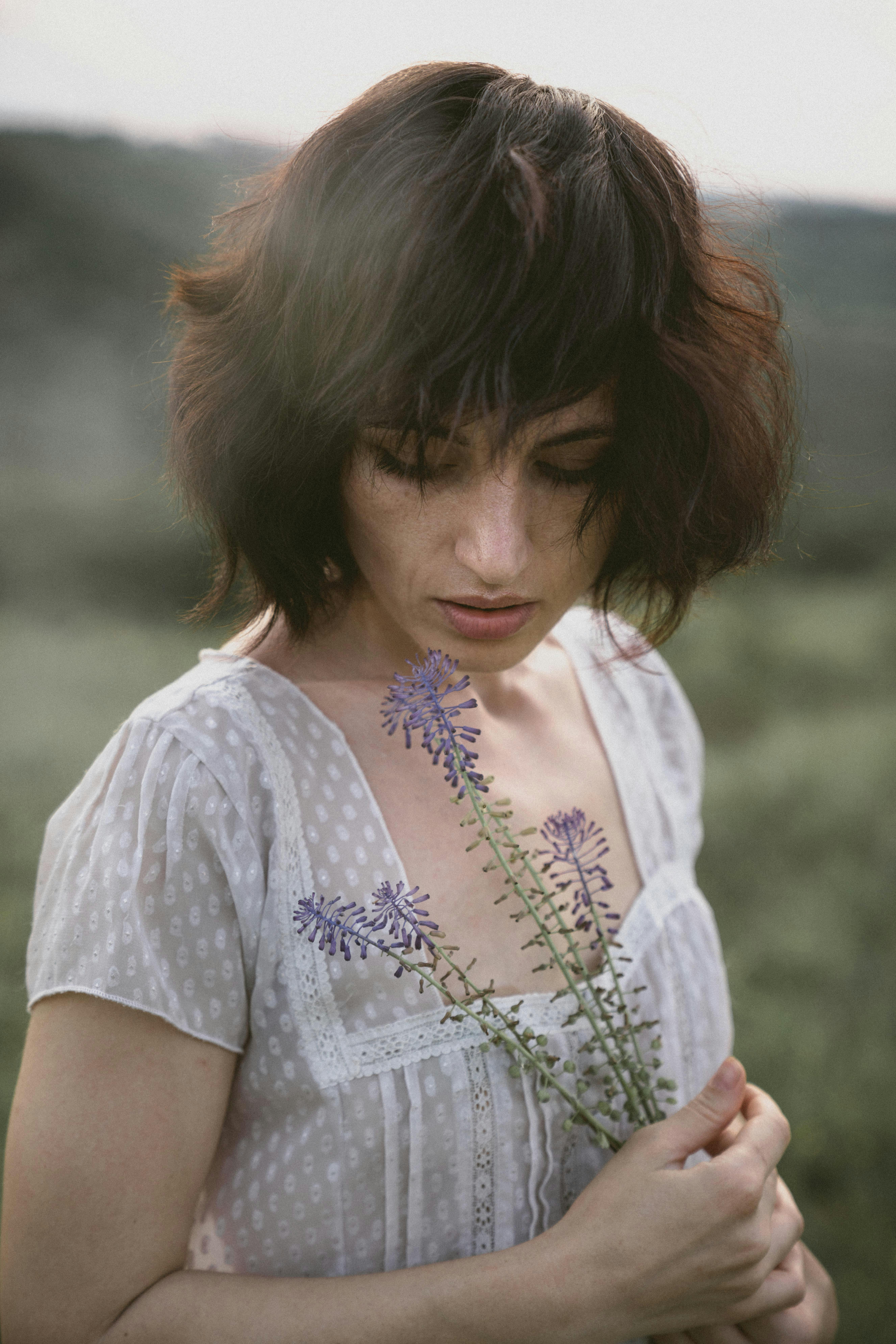 A Woman Wearing a White Dress Holing a Purple Flower · Free Stock Photo