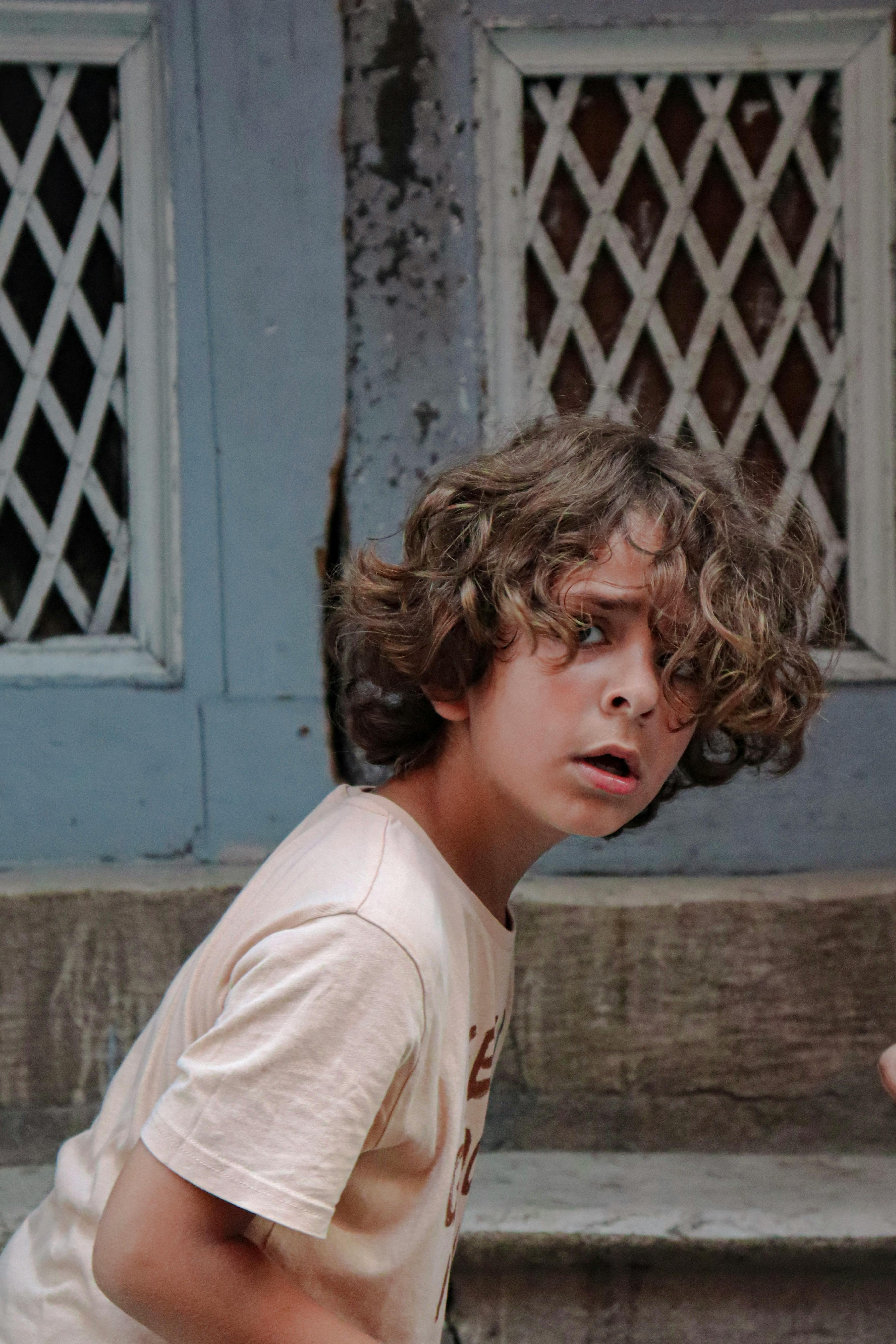 A Boy with Curly Hair Holding a Battery Operated Toy while Looking at ...
