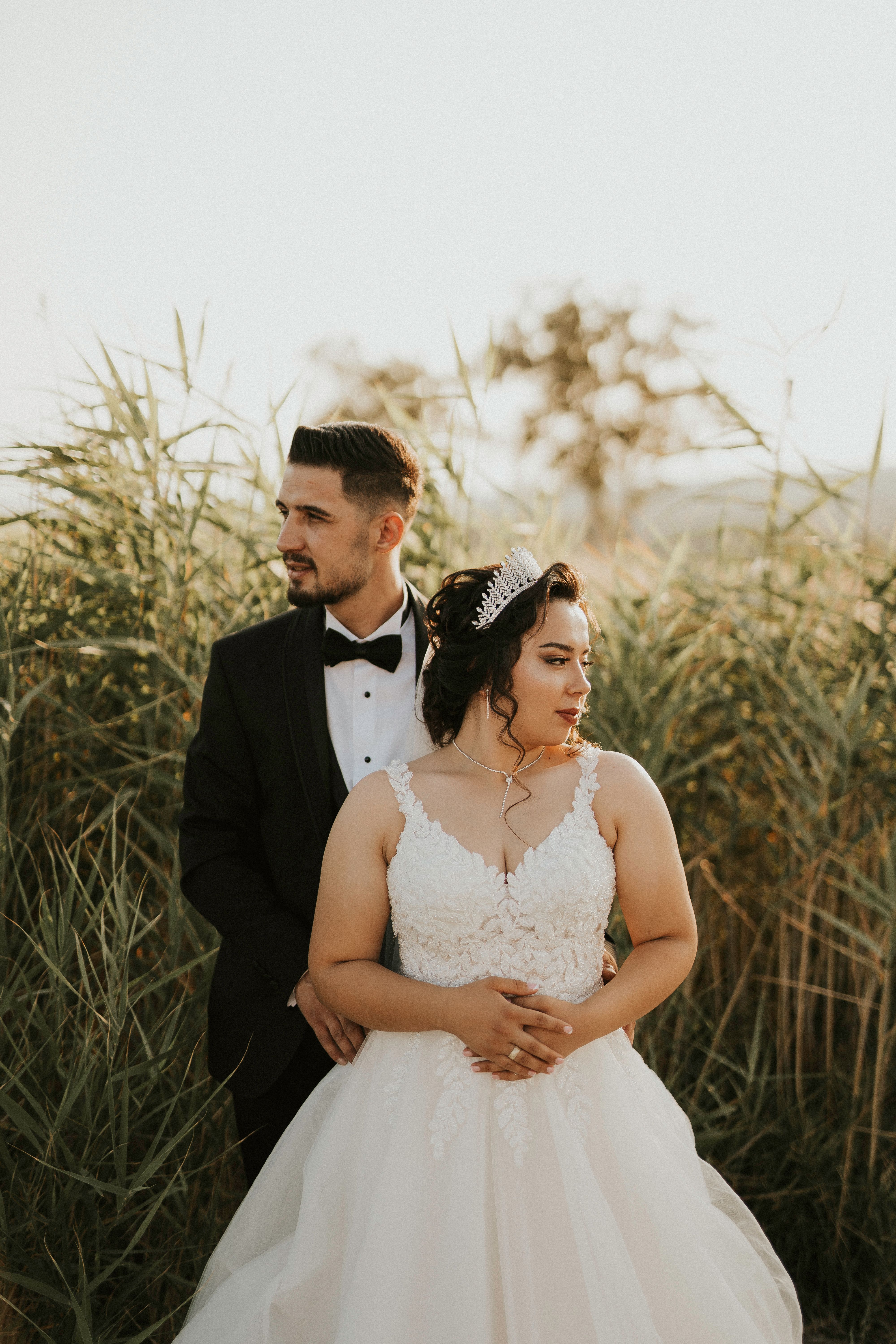 Bridegroom Holding his Bride by the Tall Grass · Free Stock Photo