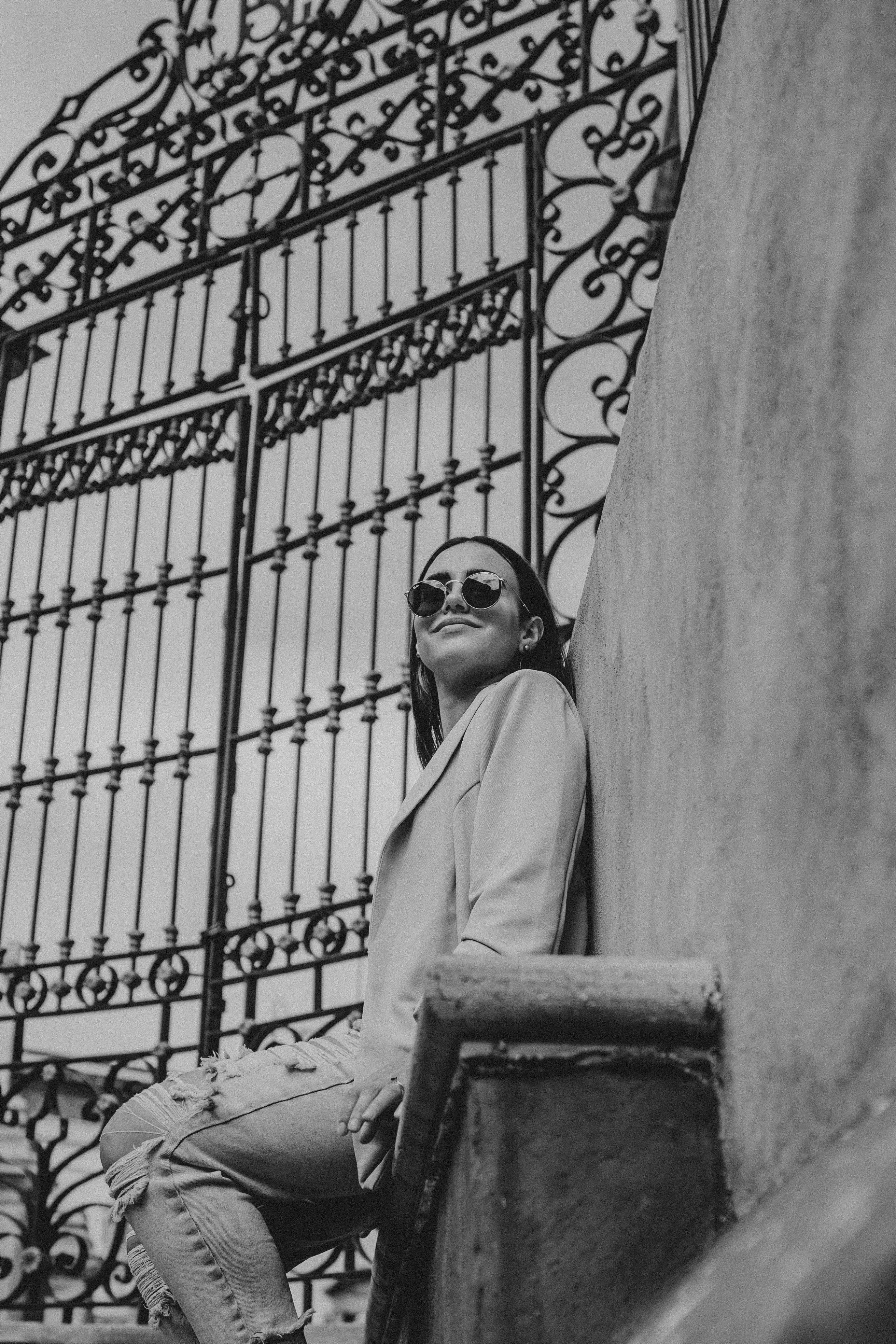 Woman Sitting in Front of a Gate in Black and White · Free Stock Photo