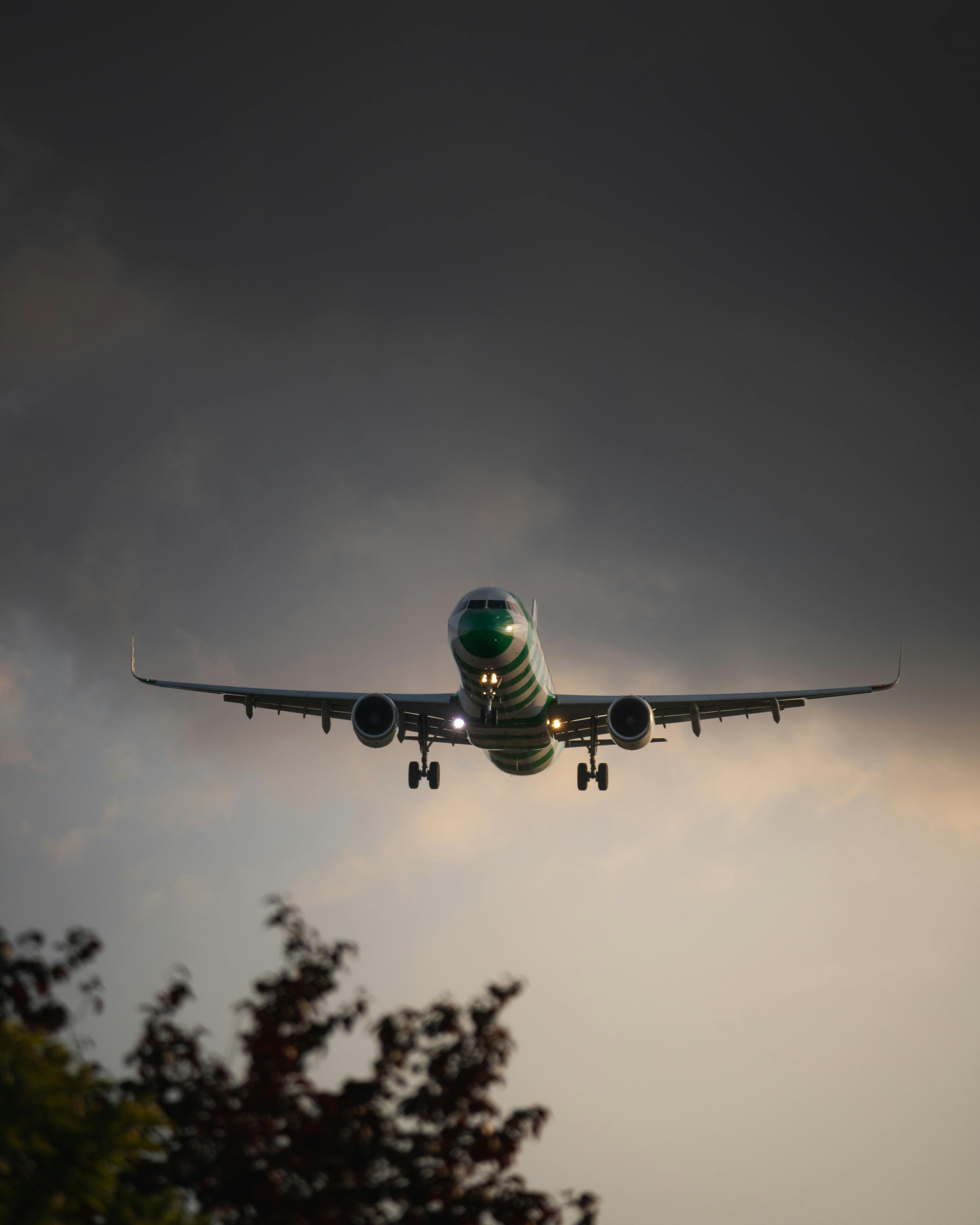 White and Green Airplane Flying Under Gloomy Sky · Free Stock Photo