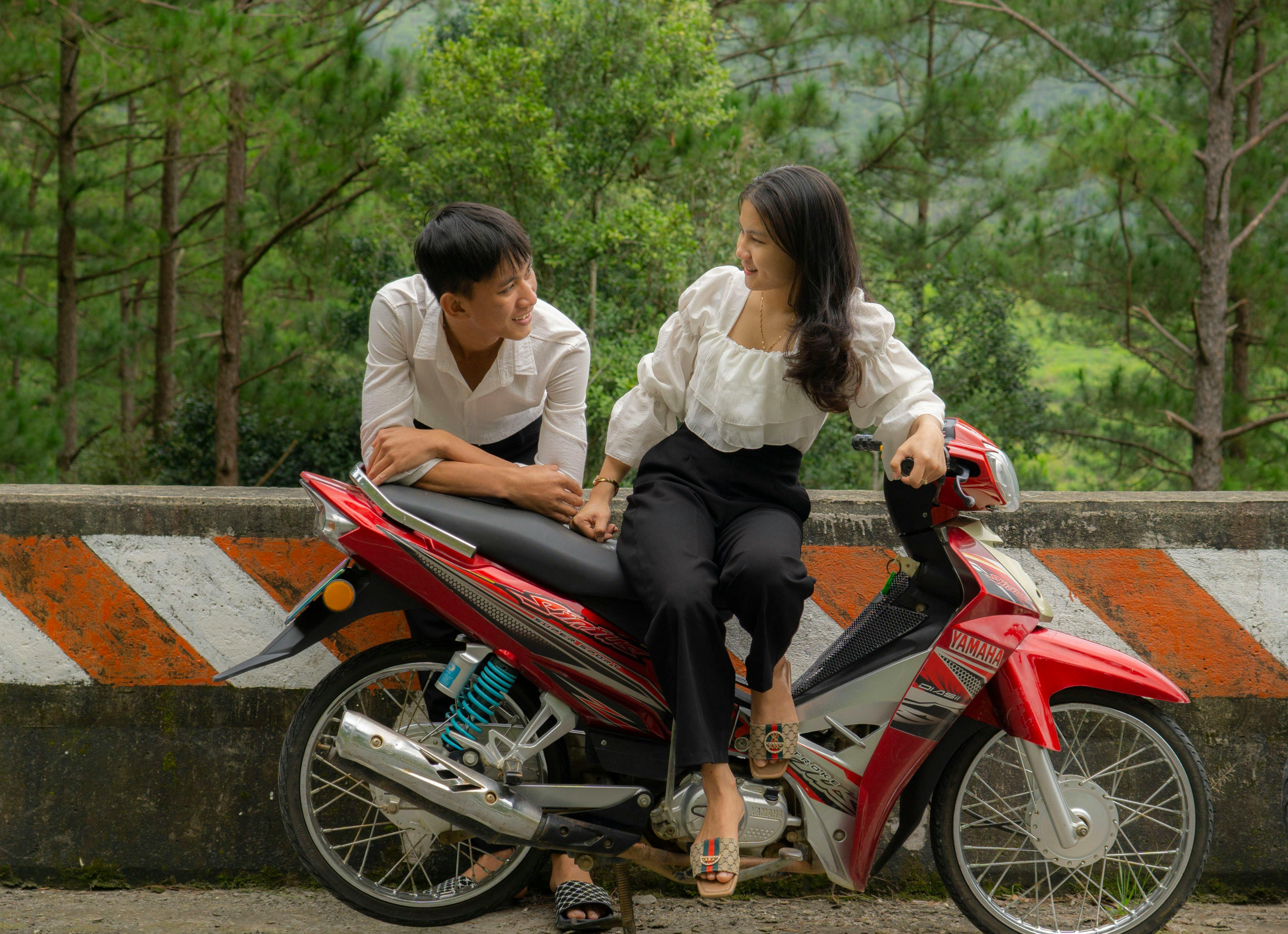 Woman in White Long Sleeve Top Sitting on Red Motorcycle Beside a Man ...