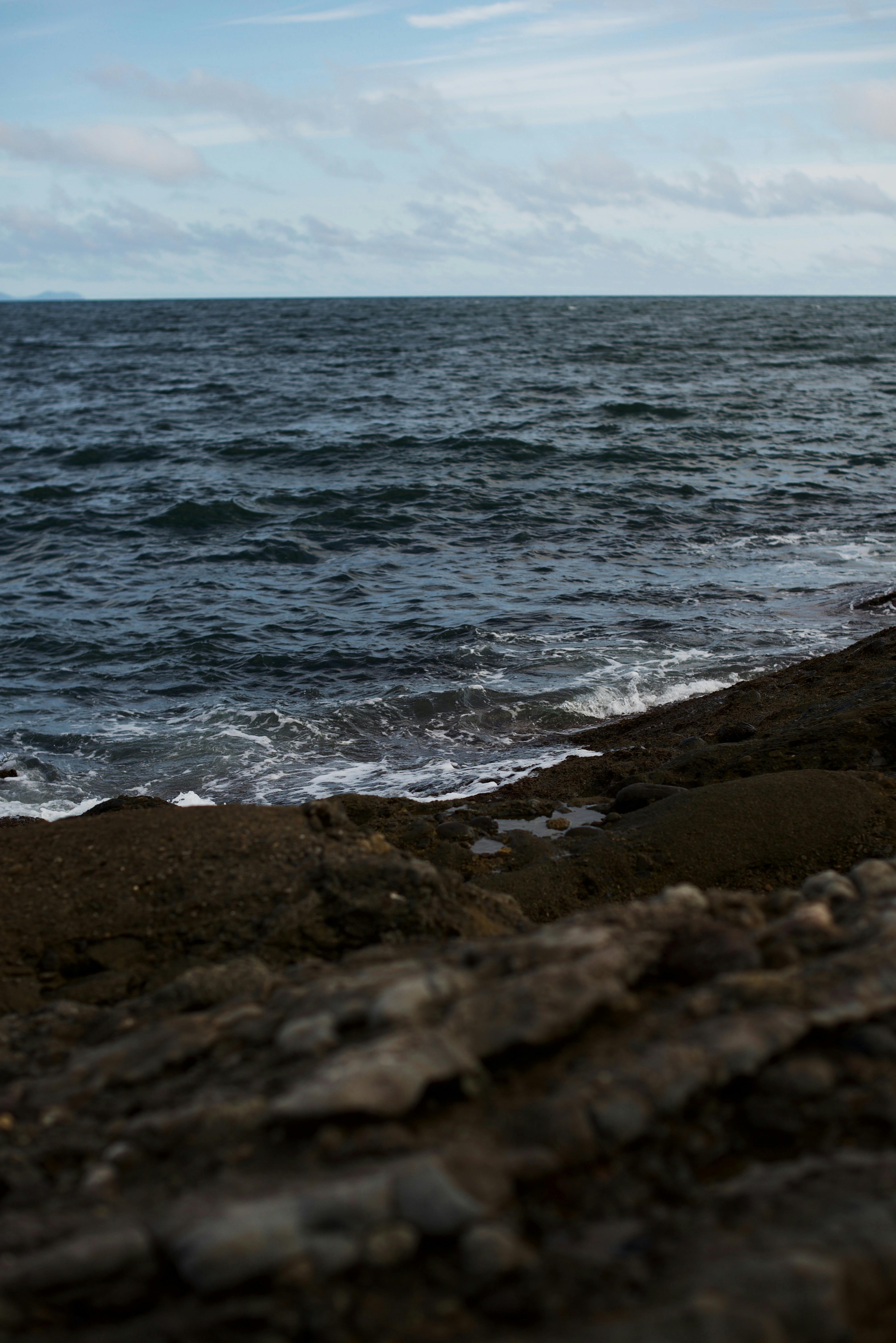 Waves Crashing onto Sea Shore with Lighthouse in Backg · Free Stock Photo