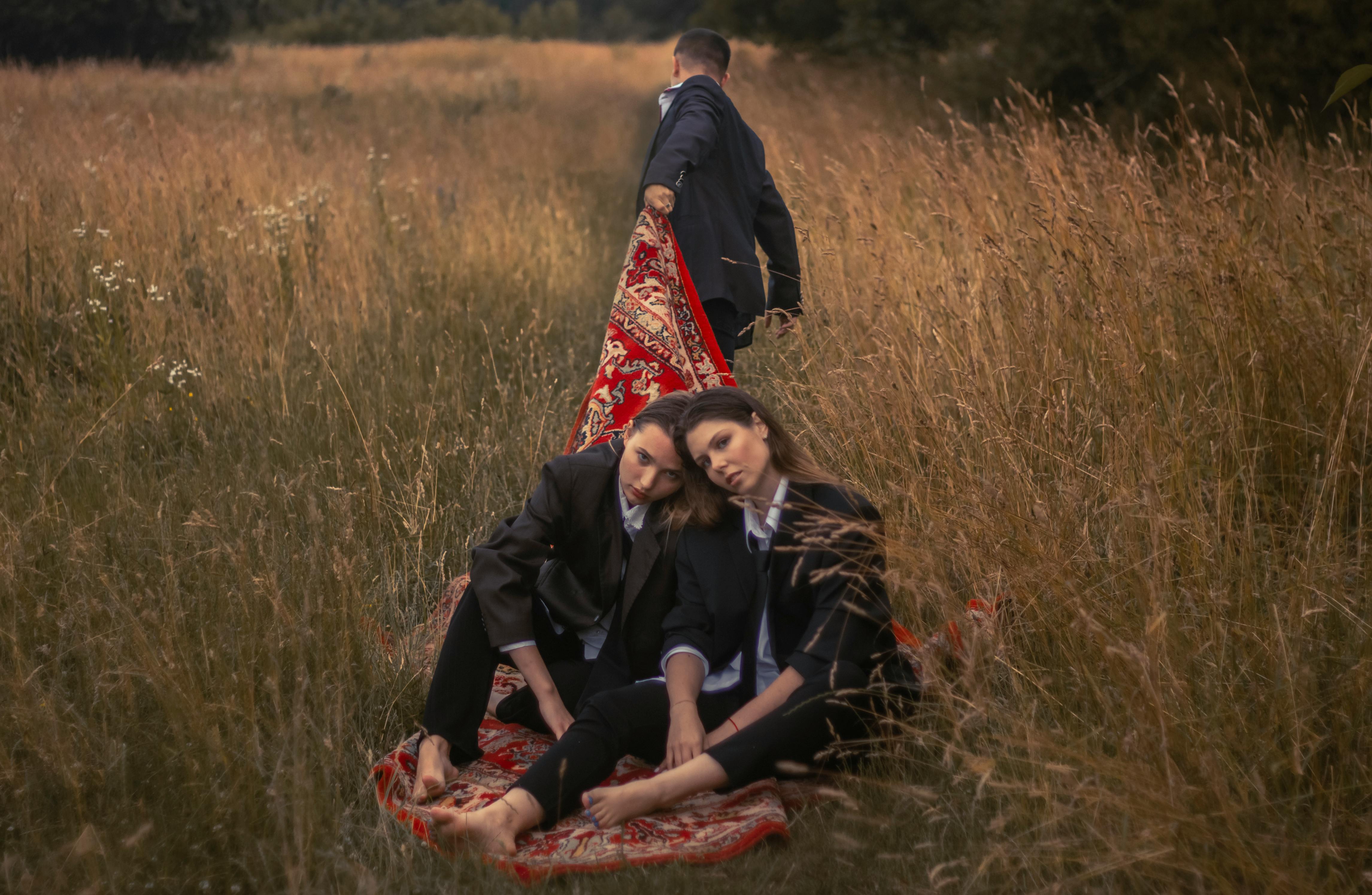 Man Pulling a Carpet with Women Sitting on It on a Field · Free Stock Photo