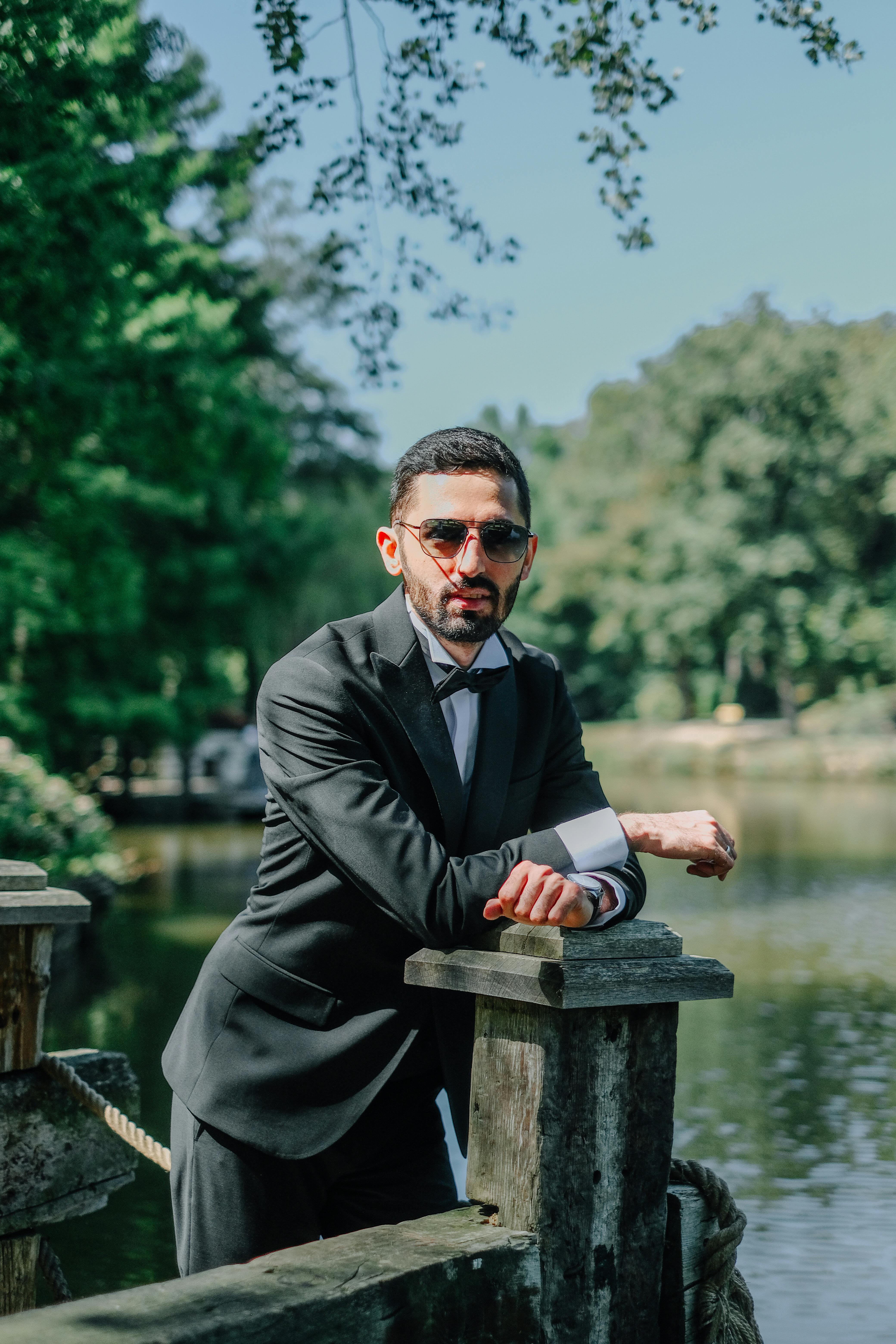 Man in Black Suit leaning on a Wooden Post · Free Stock Photo