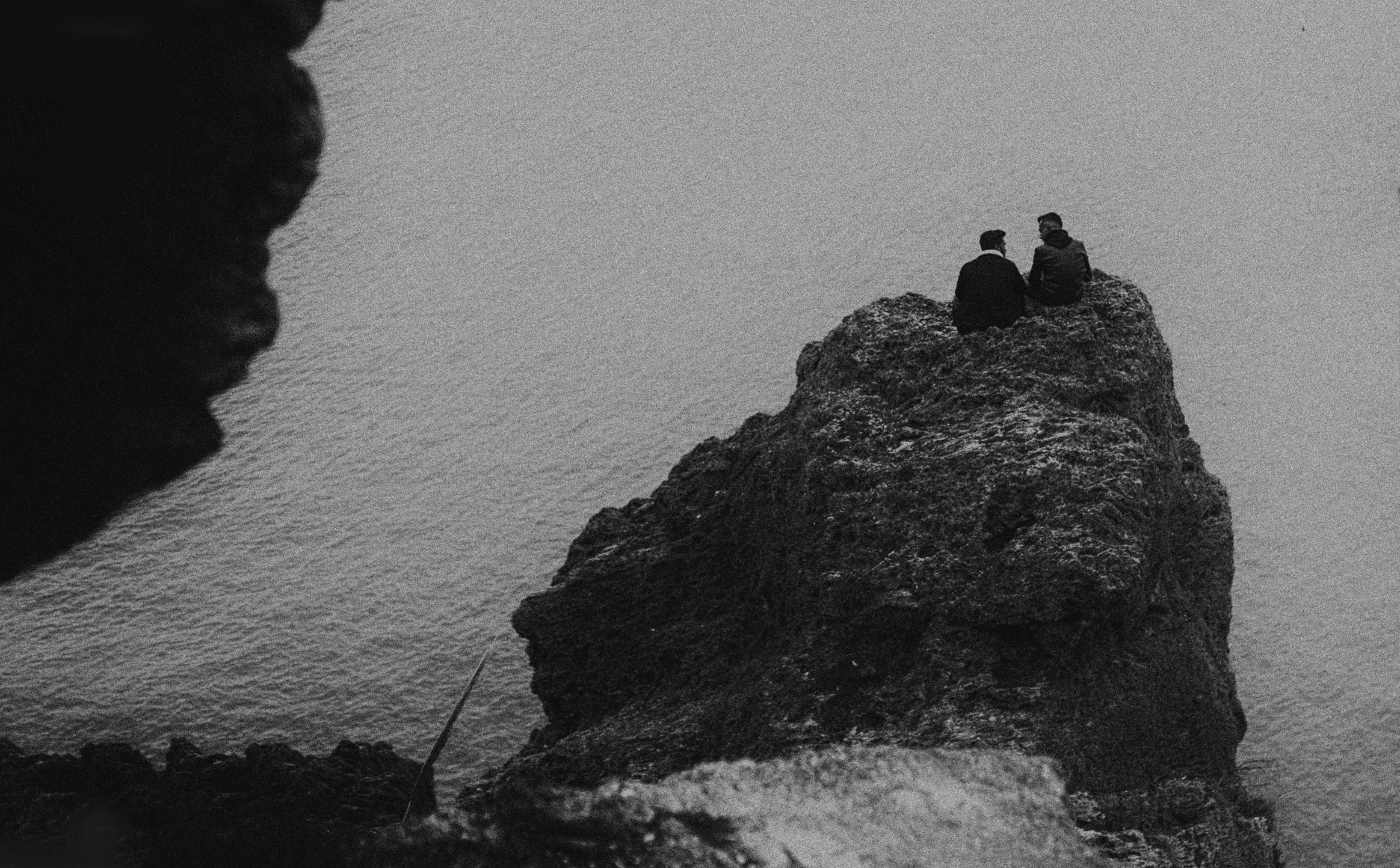 Grayscale Photo of People Sitting on a Cliff · Free Stock Photo
