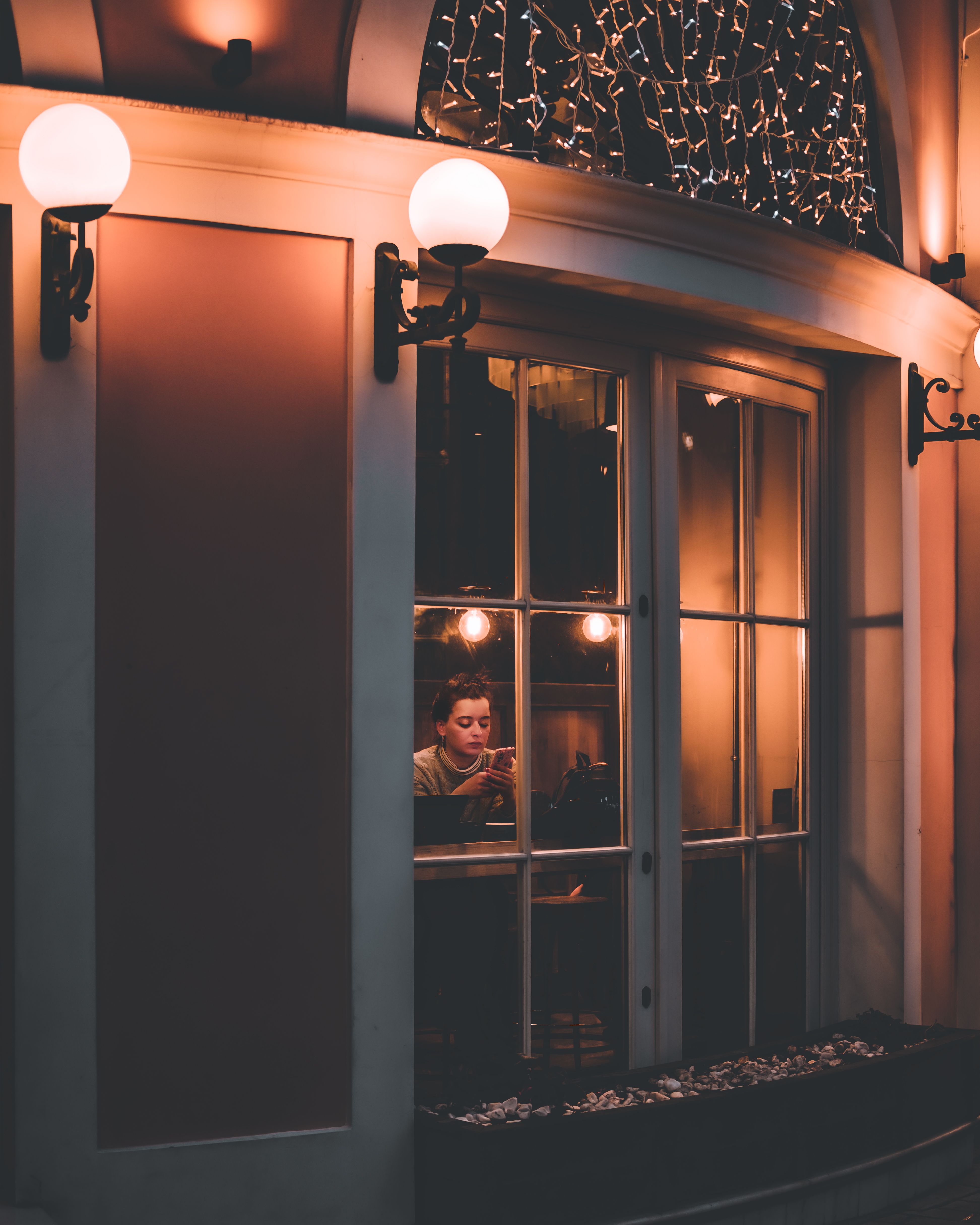 A Woman Behind the Glass Window Holding a Mobile Phone · Free Stock Photo