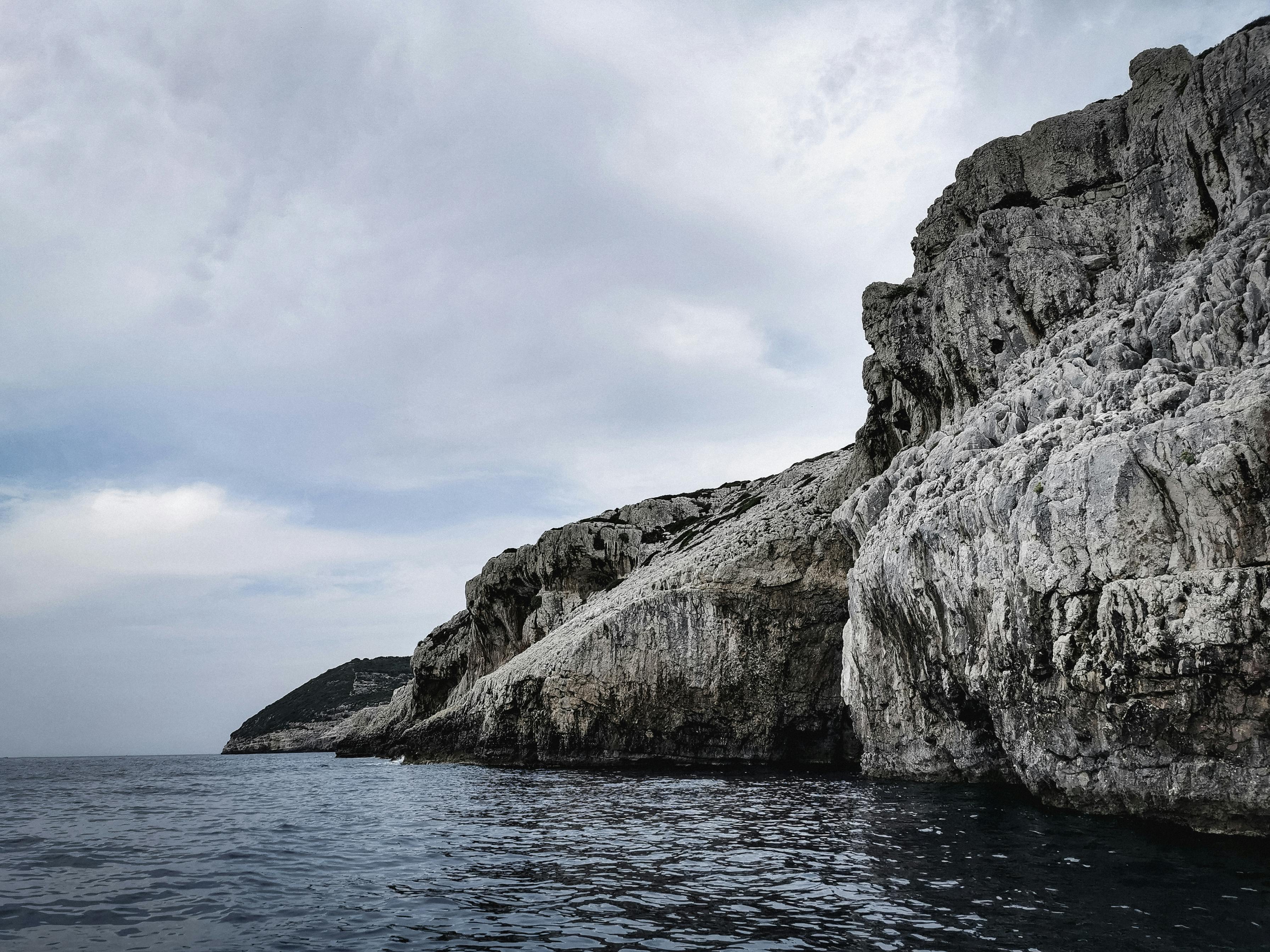 Gray Rock Formation on Sea Under White Sky · Free Stock Photo
