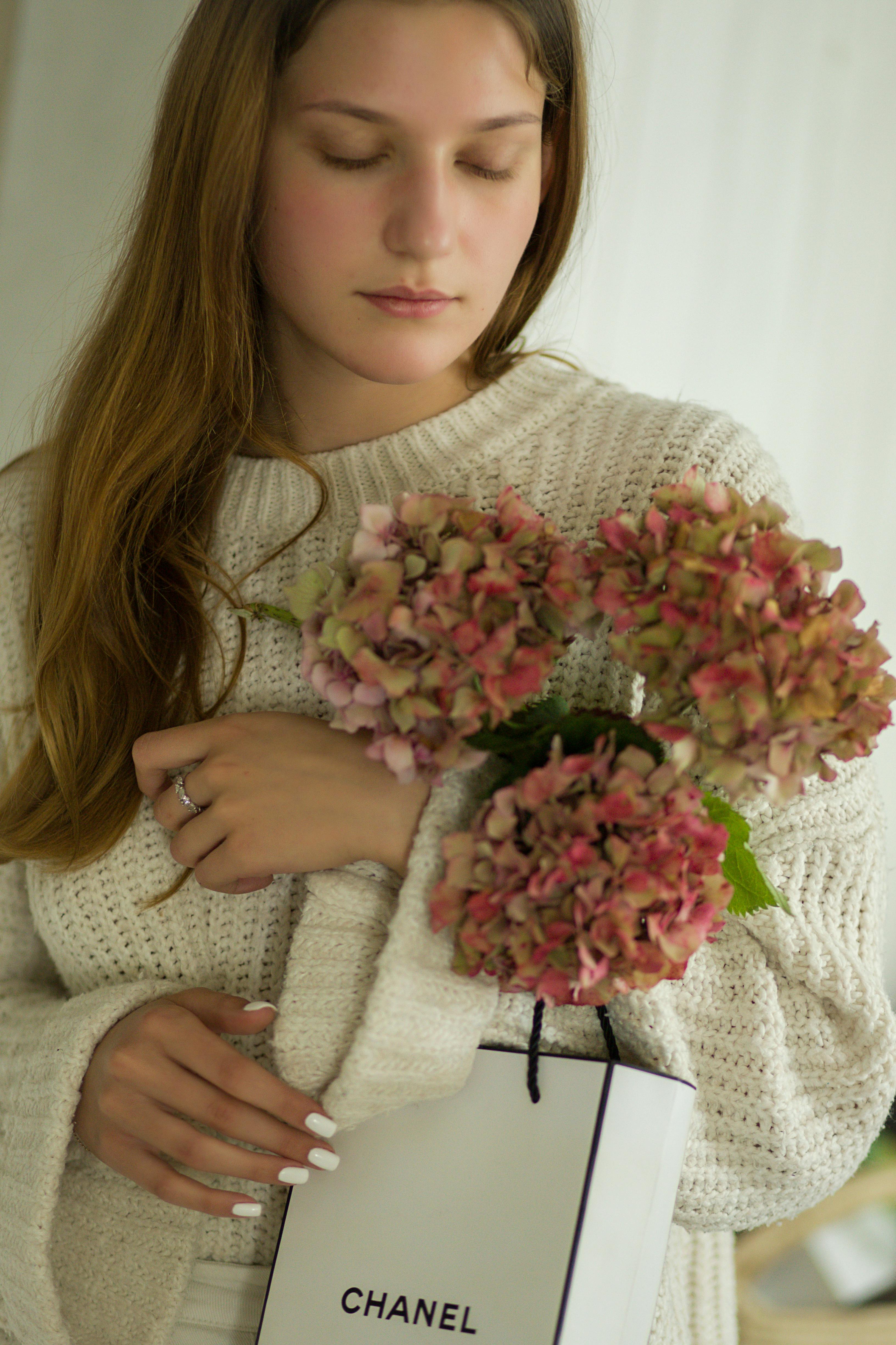 A Woman in a Knitted Sweater Holding a Paper Bag and Hydrangea Flowers ...