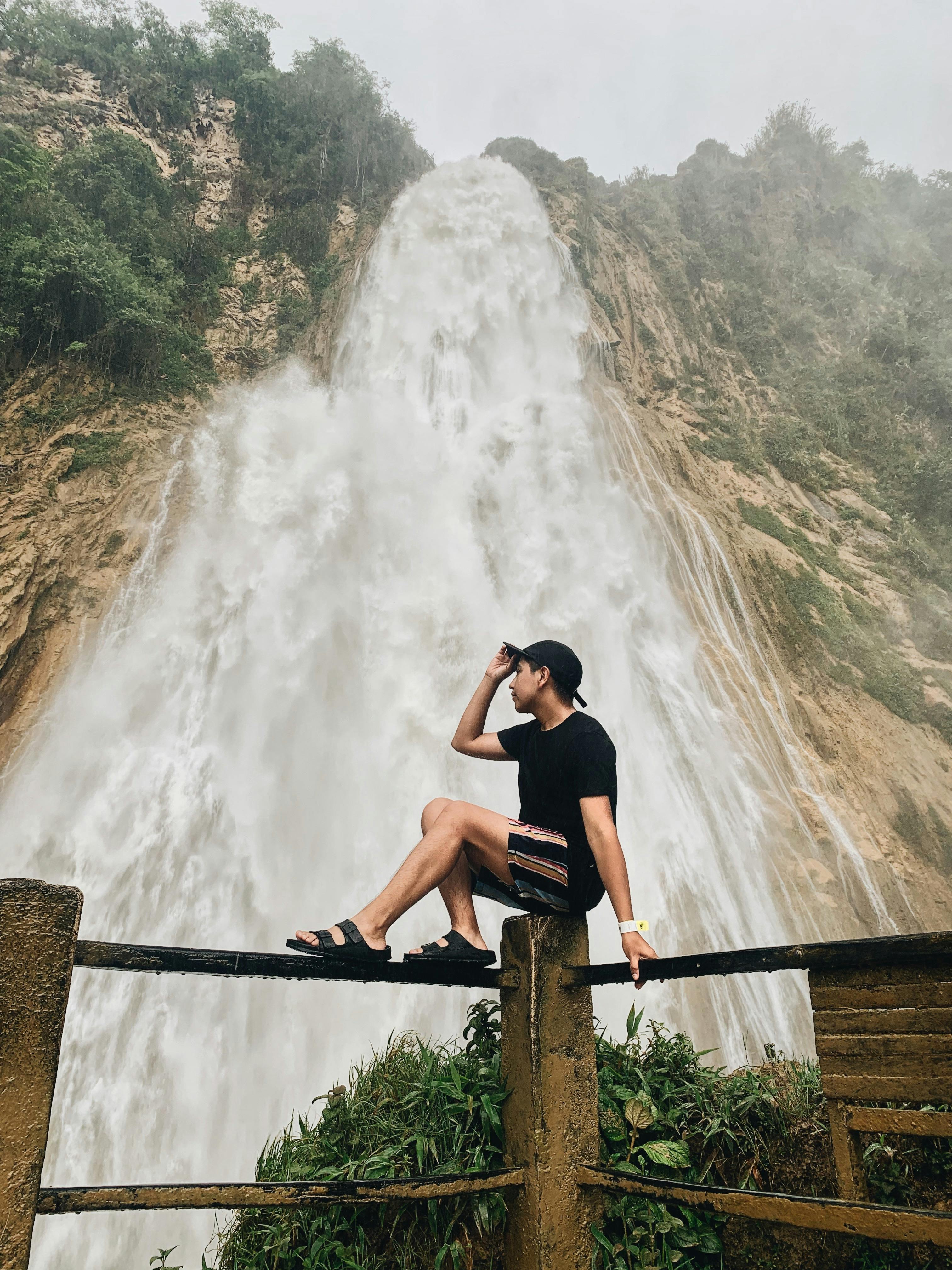 Person Sitting on Railings in Front of a Waterfalls · Free Stock Photo
