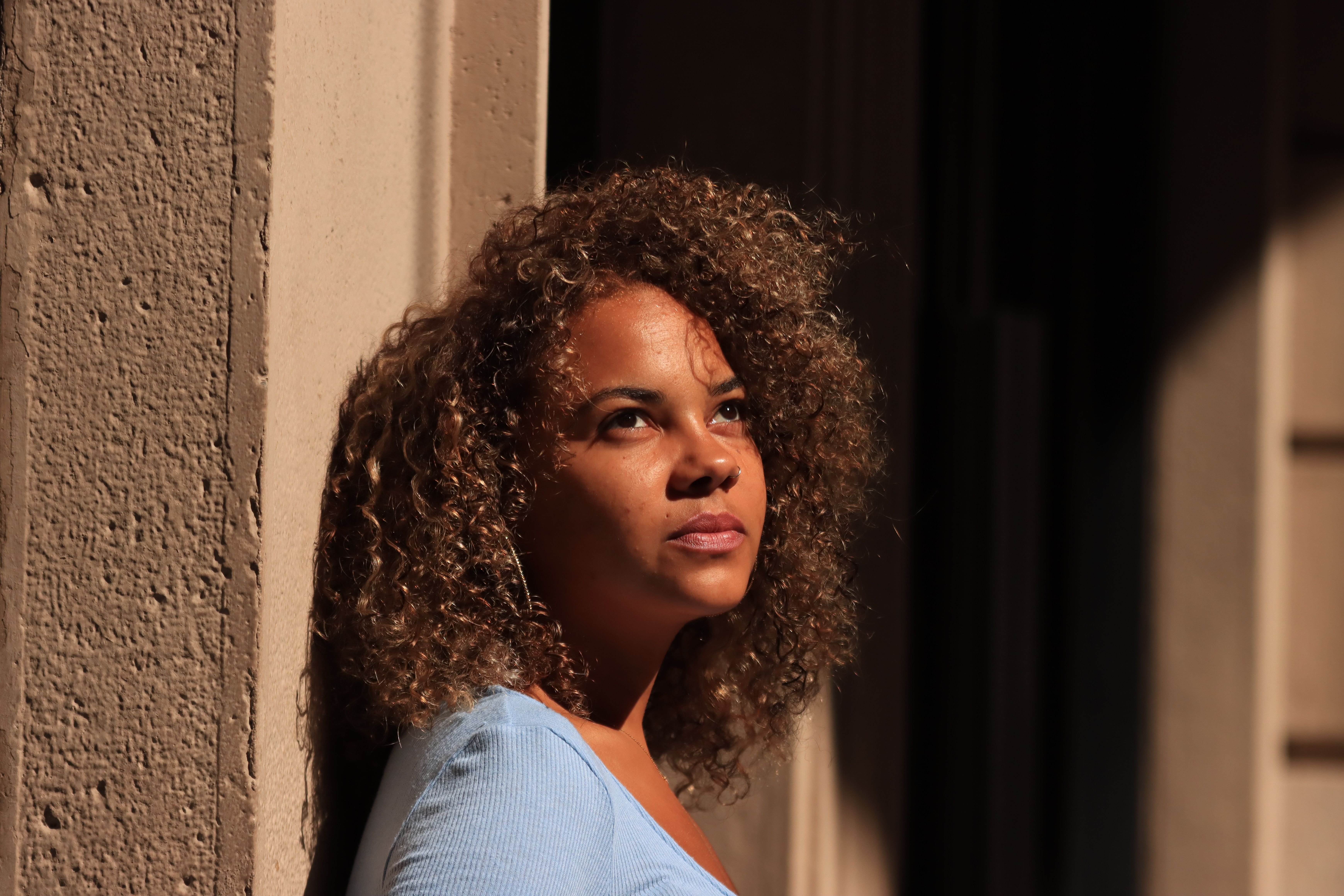 A Woman with Curly Hair Leaning on a Concrete Wall · Free Stock Photo