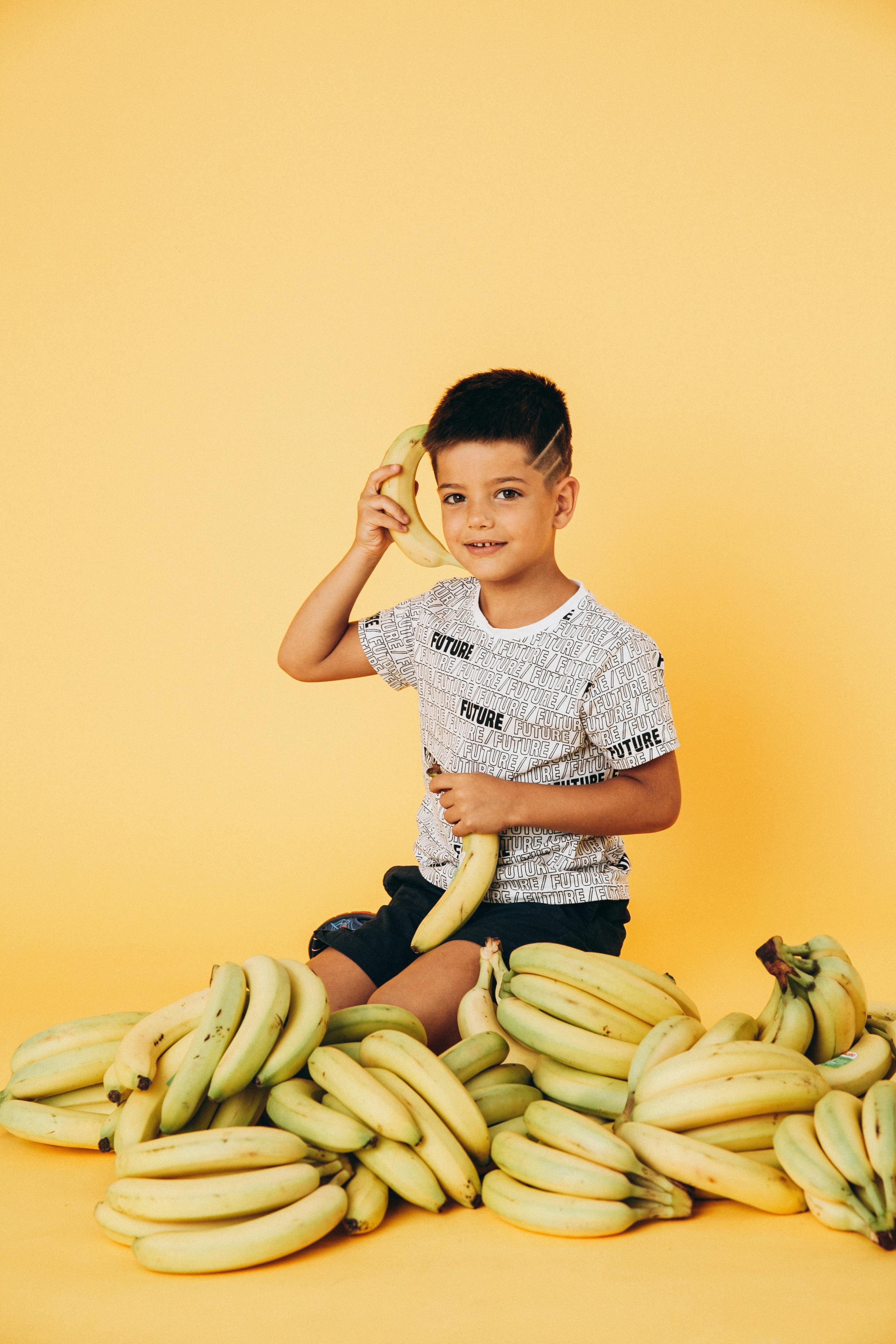 A Young Boy Sitting Near the Bunch of Bananas · Free Stock Photo