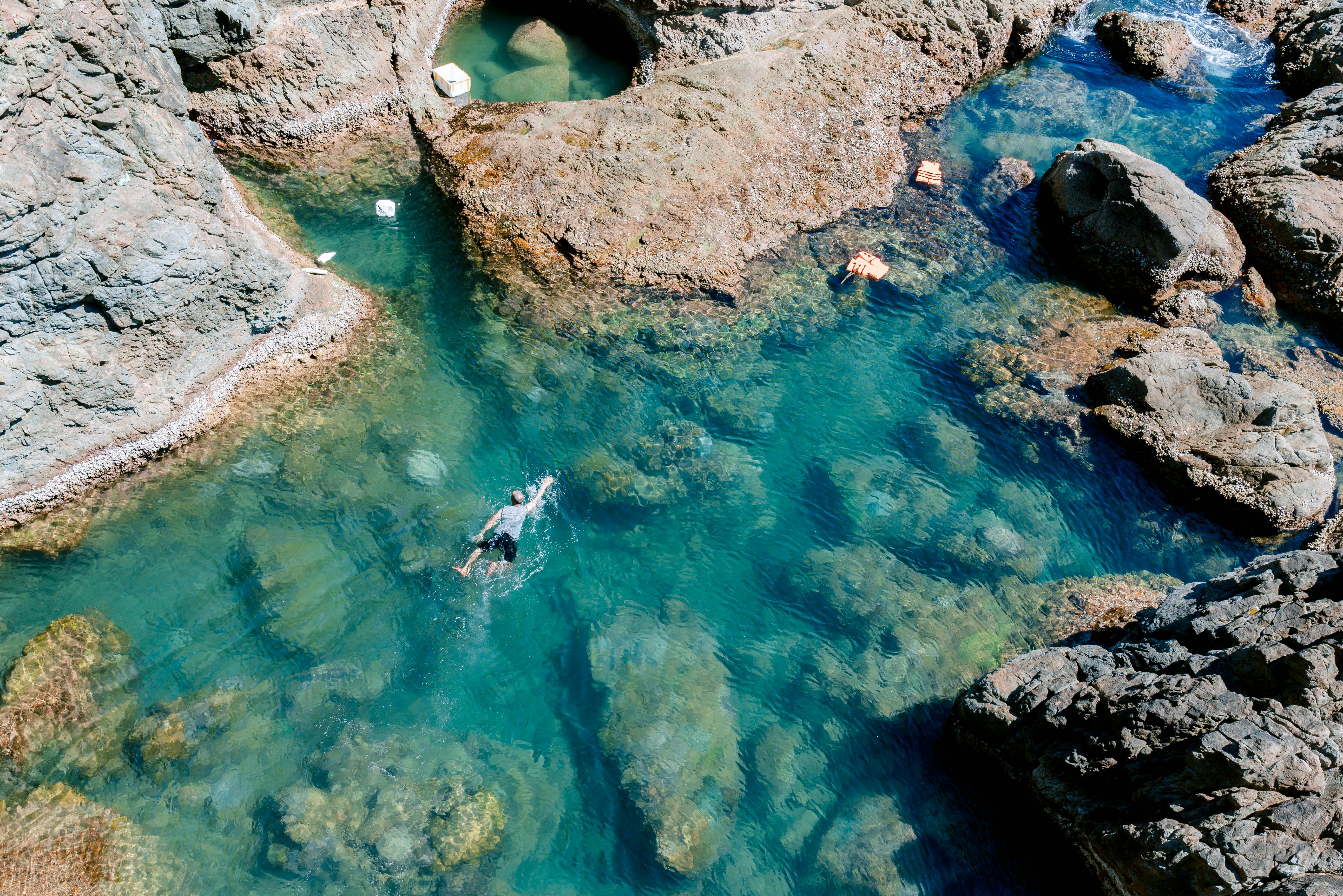 Person Swimming on Sea Around Rock Formations · Free Stock Photo