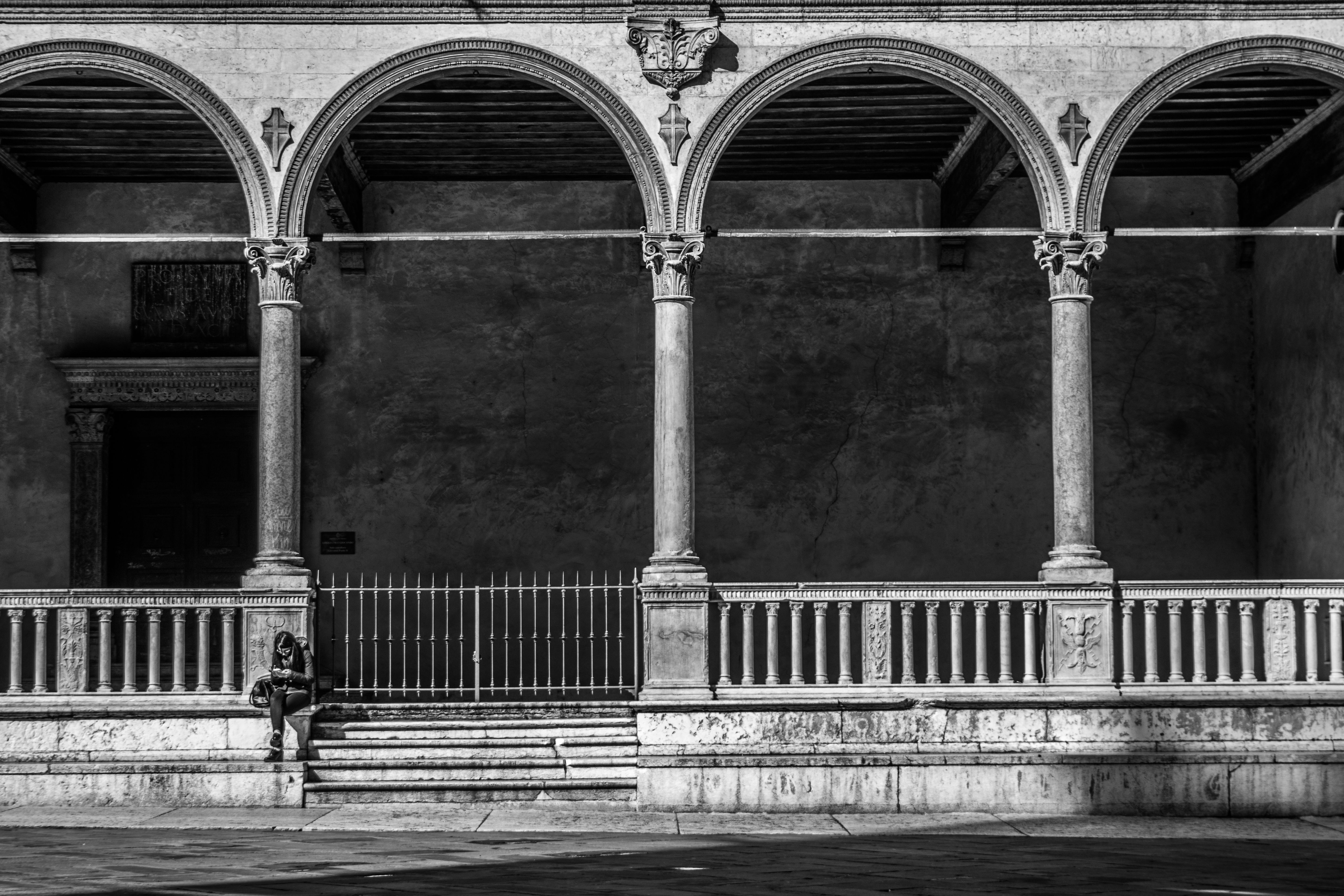 Woman Sitting near Gate in Black and White · Free Stock Photo