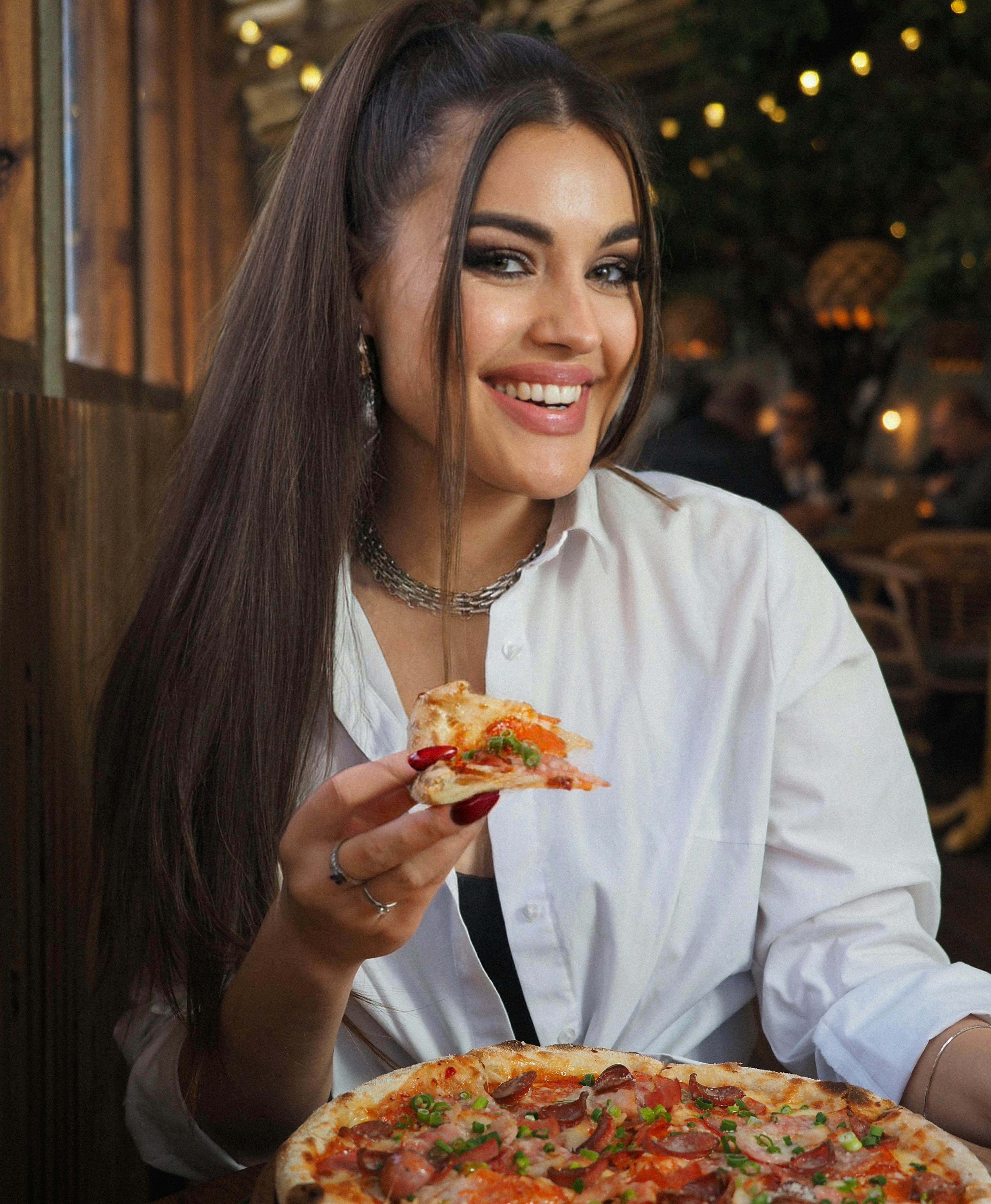 A Pretty Woman in a White Top Eating Pizza · Free Stock Photo