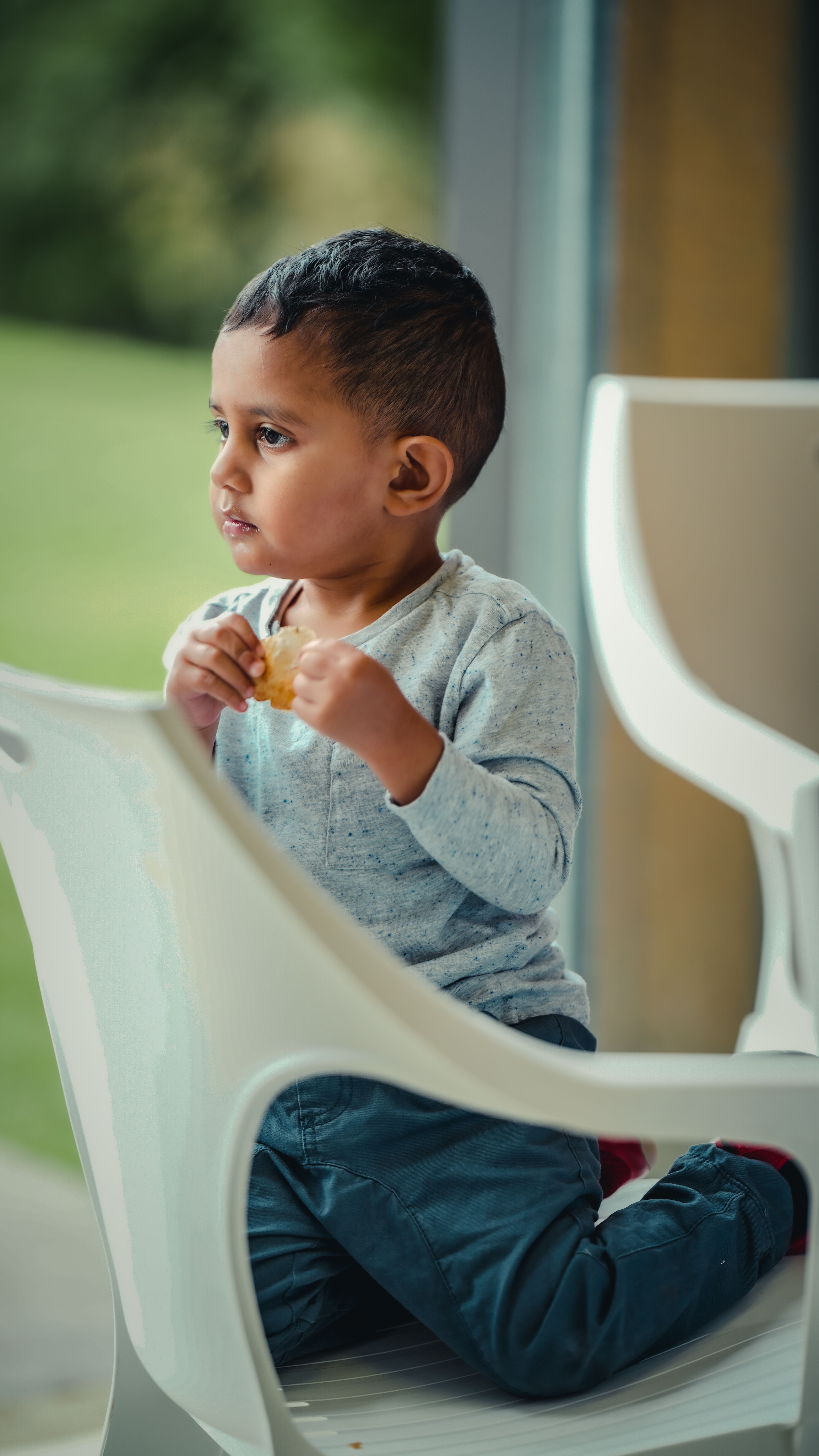 A Boy Wearing a Gray Long Sleeves Sitting on a White Chair While ...