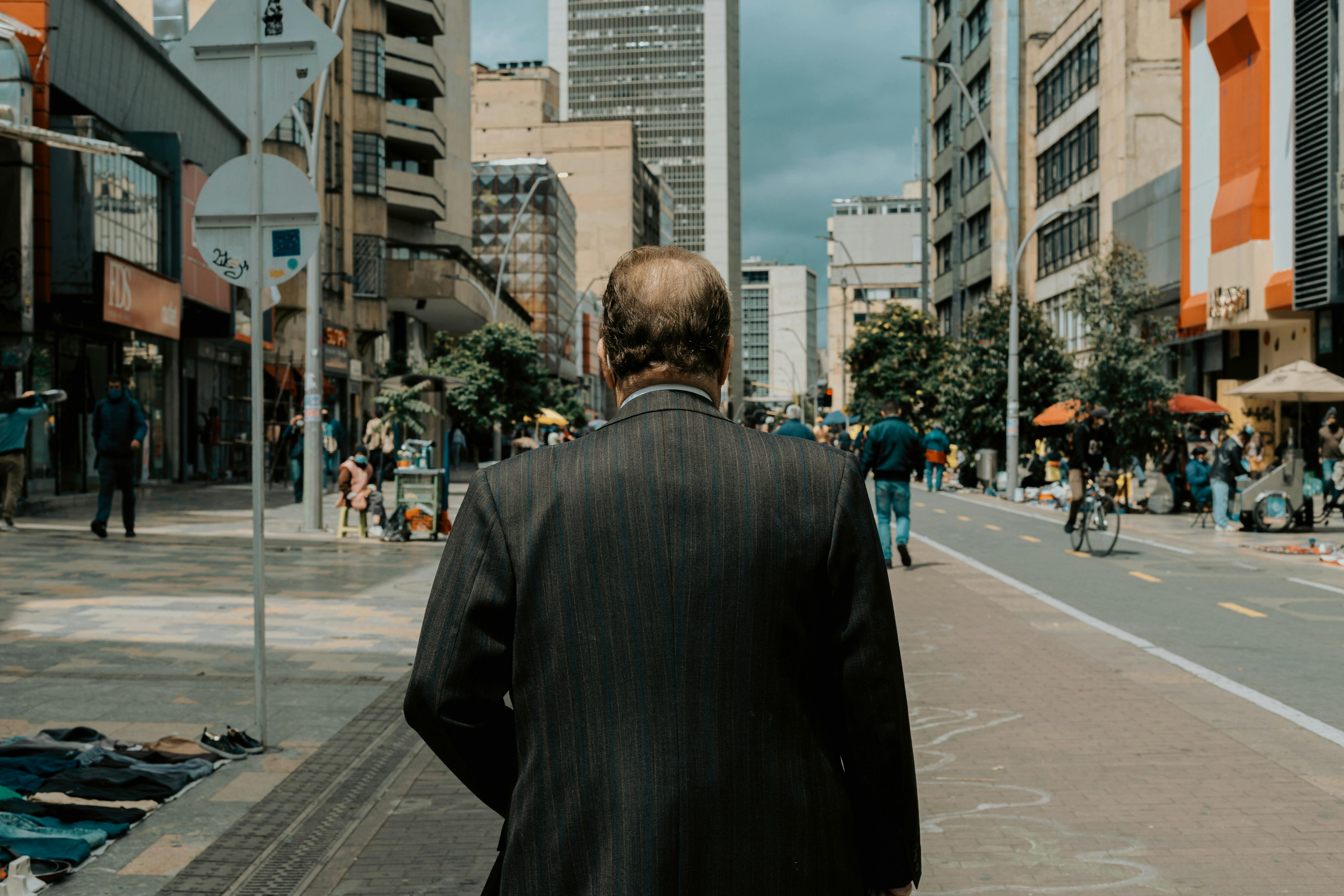 Back View Shot of a Man in Black Suit Walking on the Roadside Near City ...
