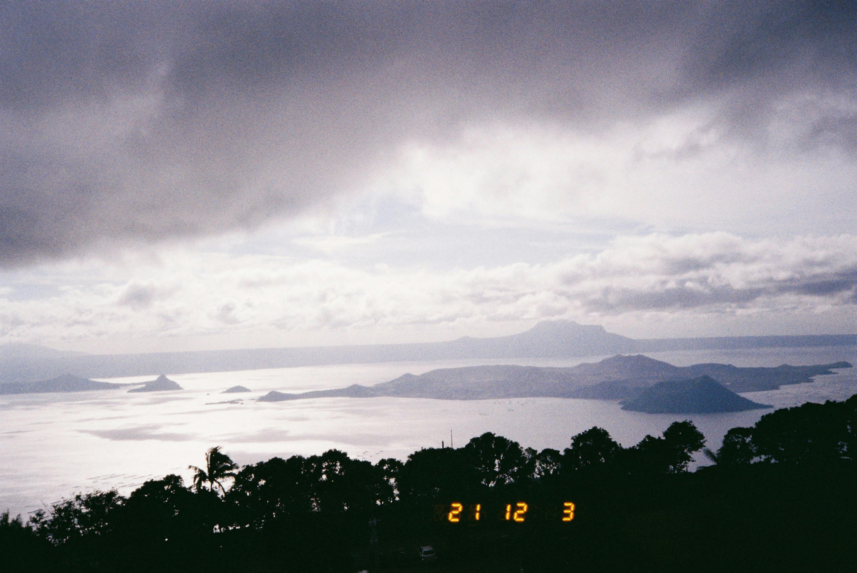 Silhouette of Trees Overlooking Small Volcano on Body of Water During ...