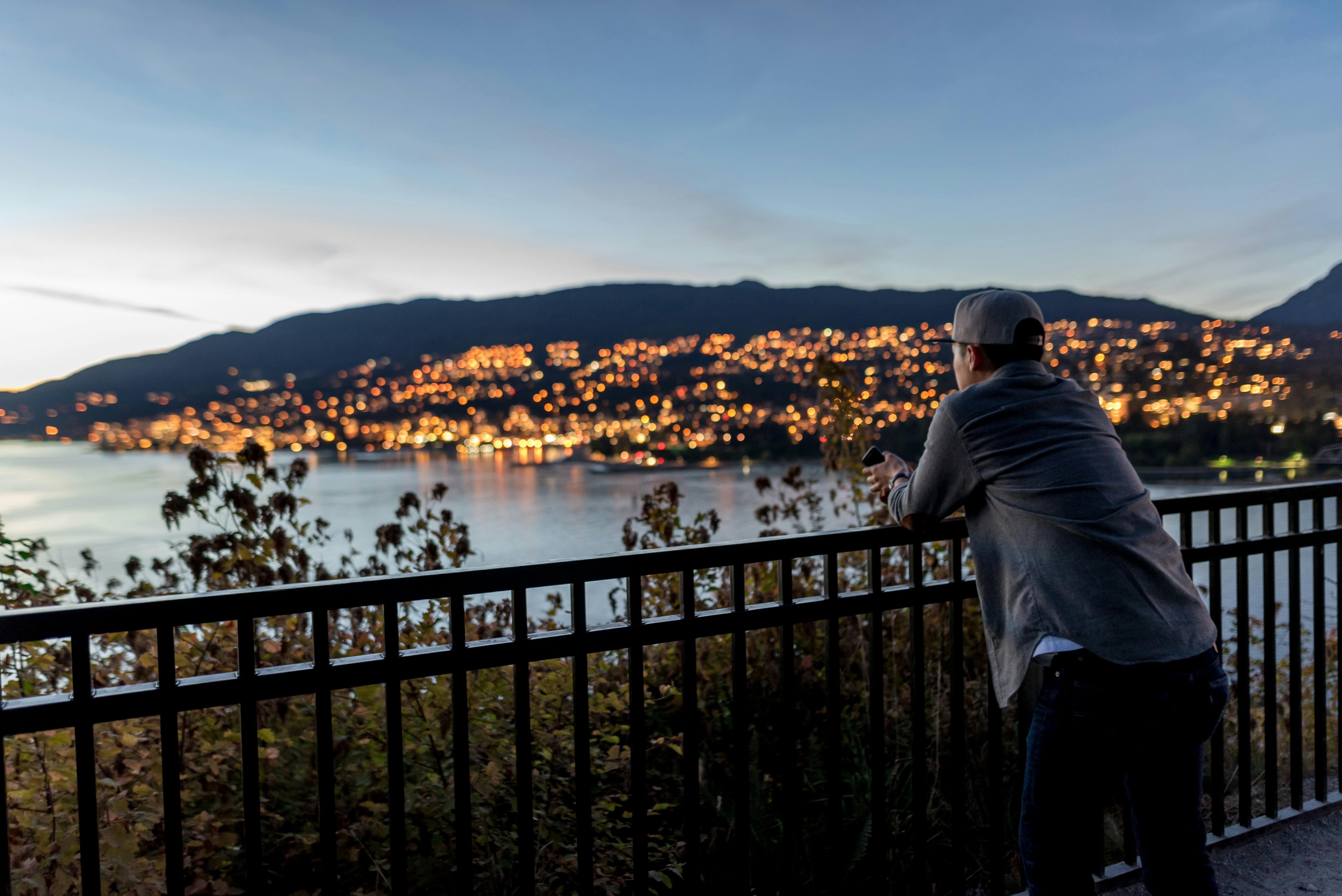 Man Looking at Sea Bay and Illuminated City · Free Stock Photo