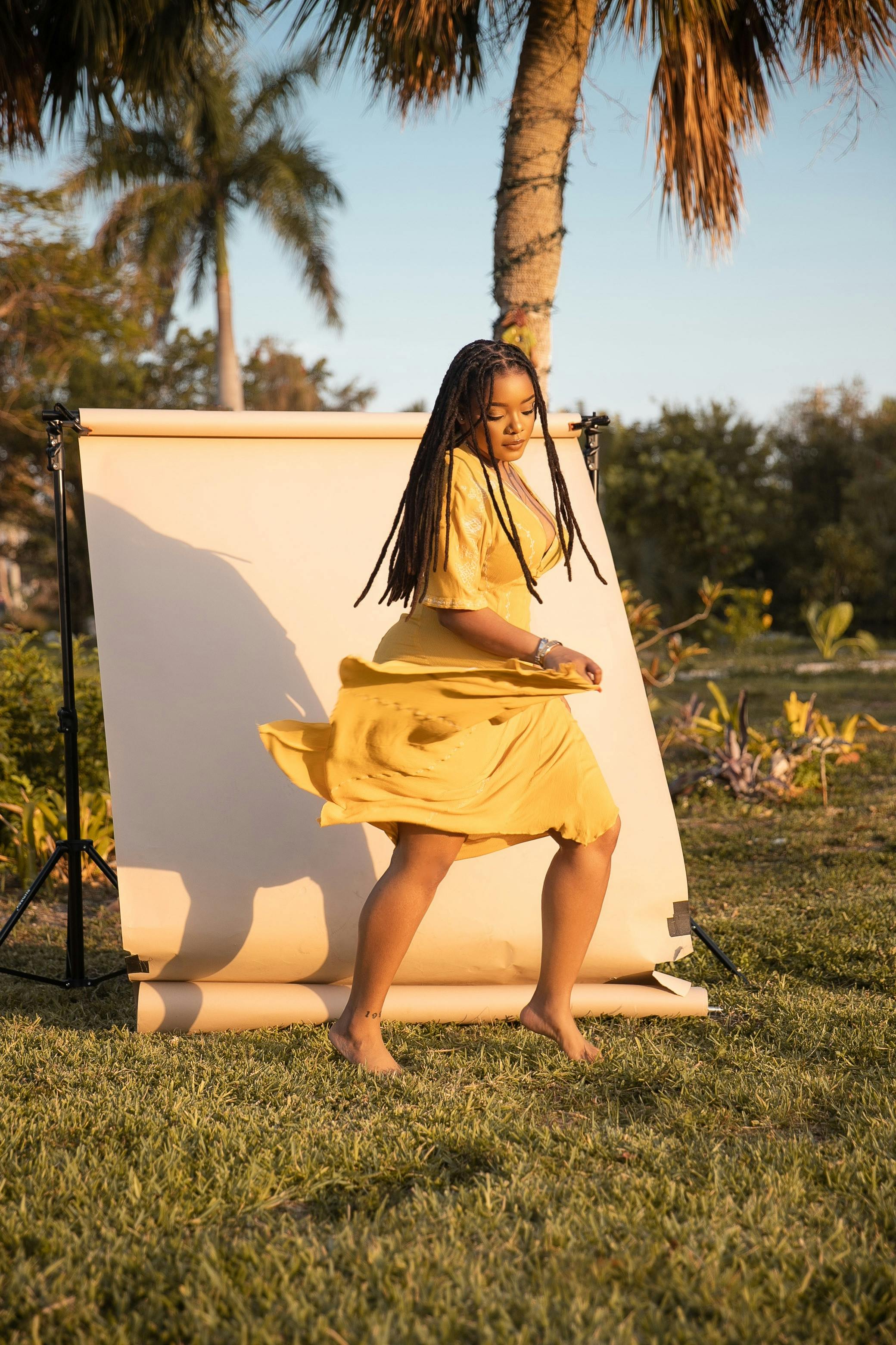 Young Woman in a Yellow Dress Posing Barefoot on the Grass near a Palm ...