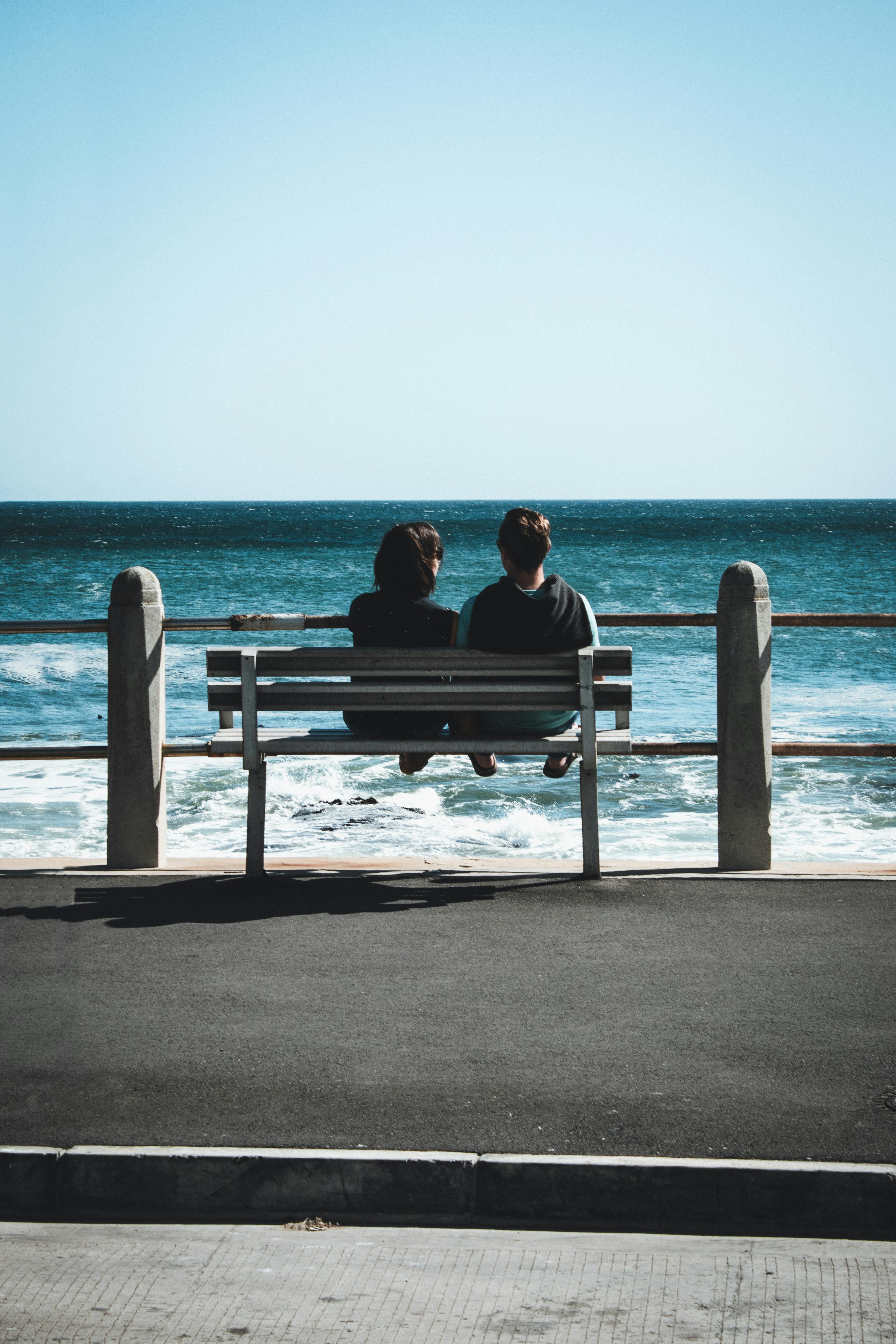 Back View of a Couple Sitting on a Bench near Sea · Free Stock Photo
