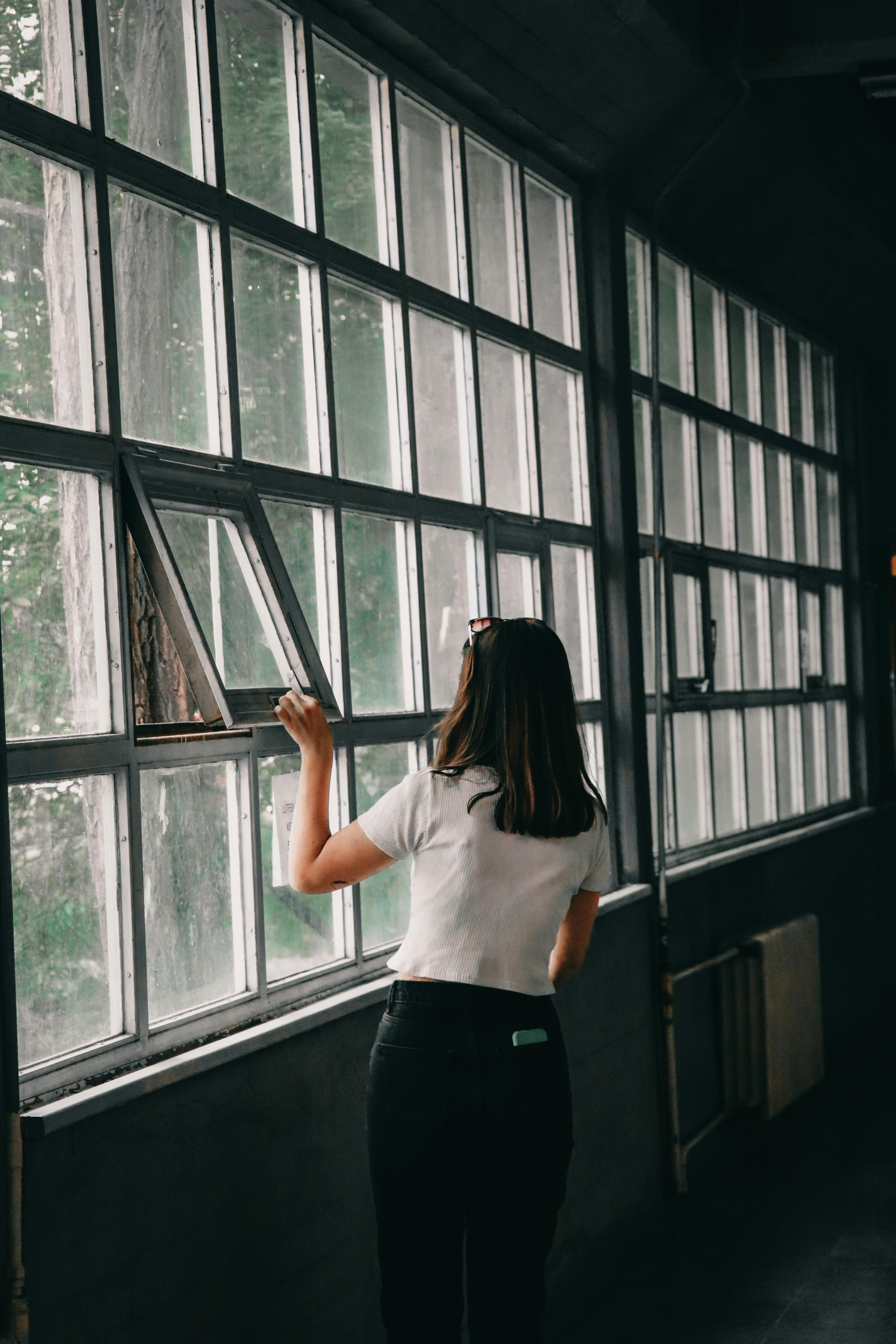 A Back View of a Woman in White Shirt Standing Near the Glass Windows ...