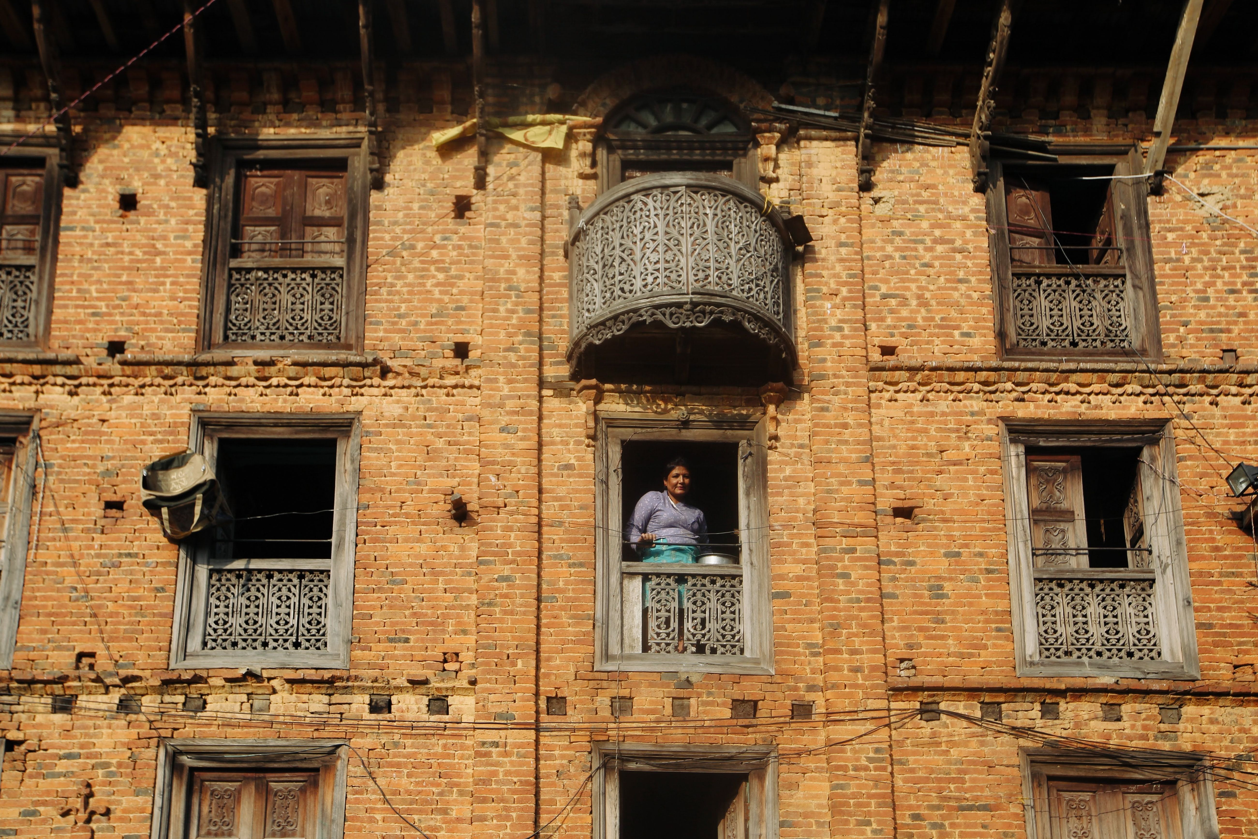 A Woman Standing on the Balcony of Brown Brick House · Free Stock Photo