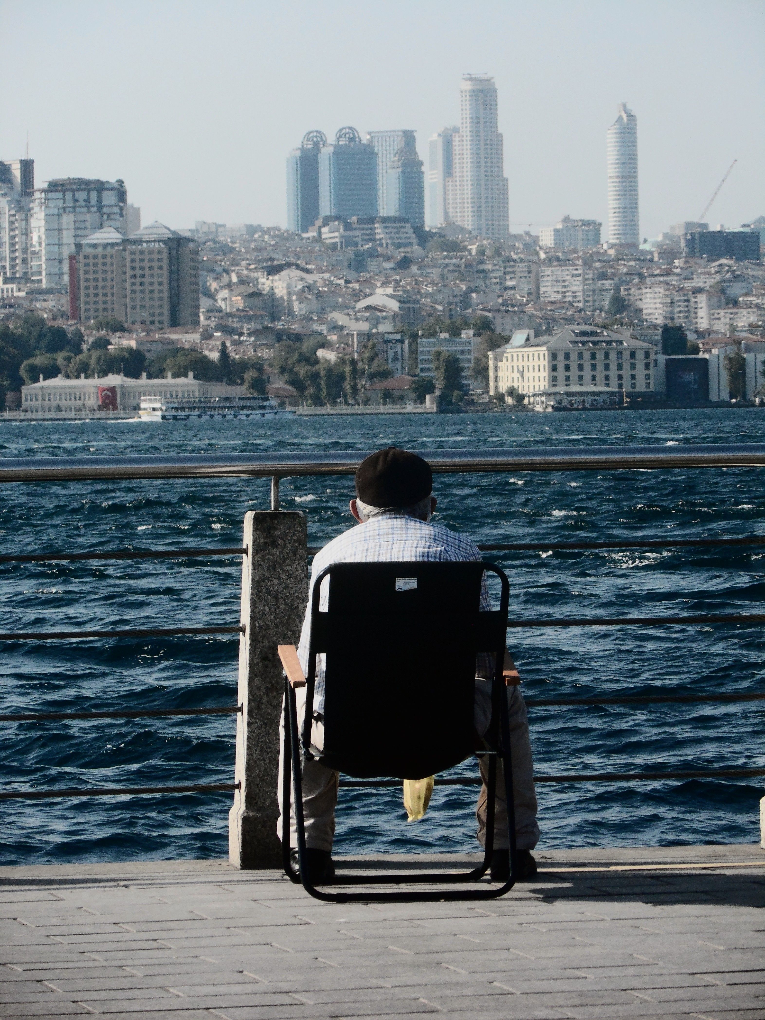 Man Sitting on Folding Chair on Bridge Overlooking City · Free Stock Photo