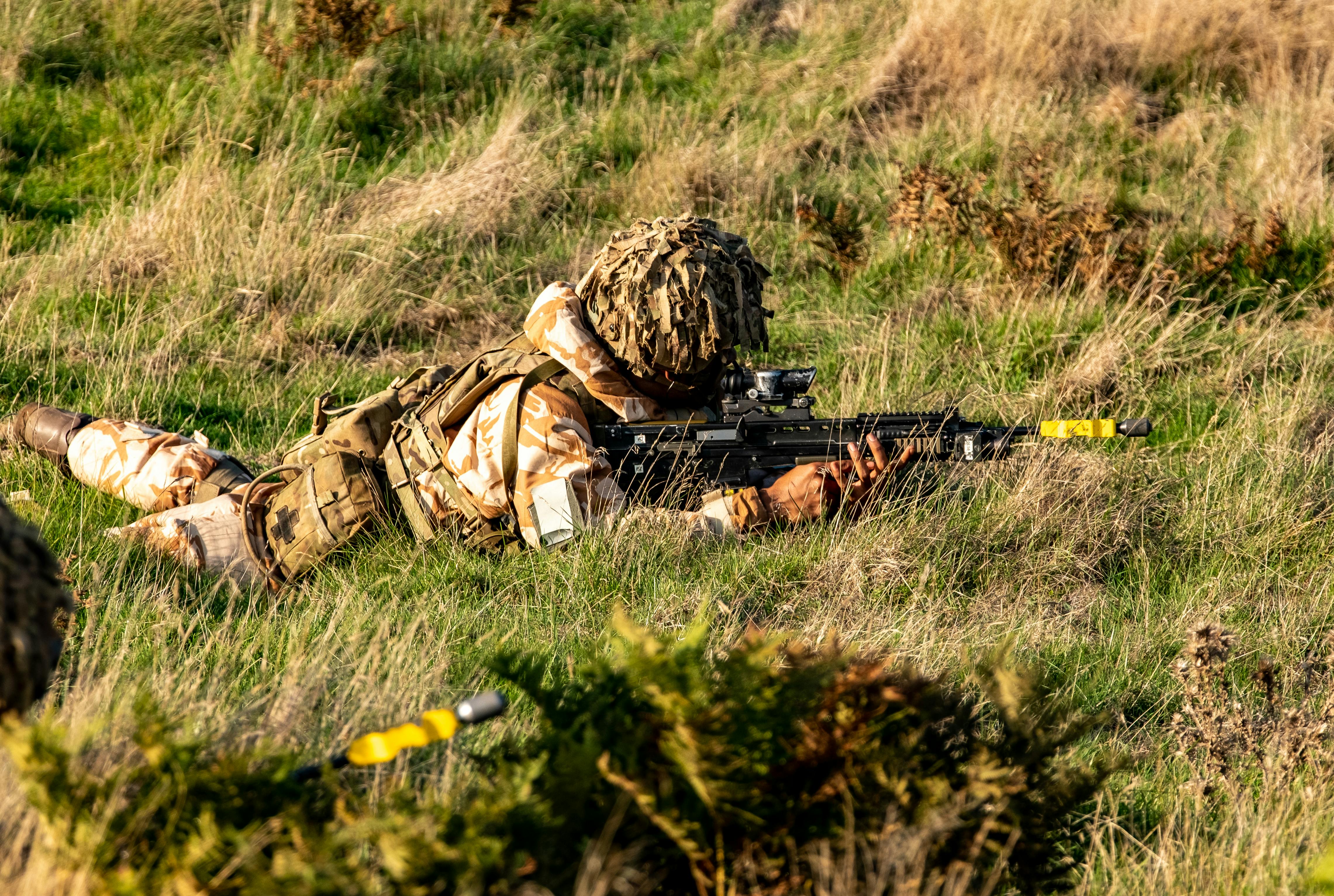 A Soldier Holding Weapon while Crawling on Grass Field · Free Stock Photo