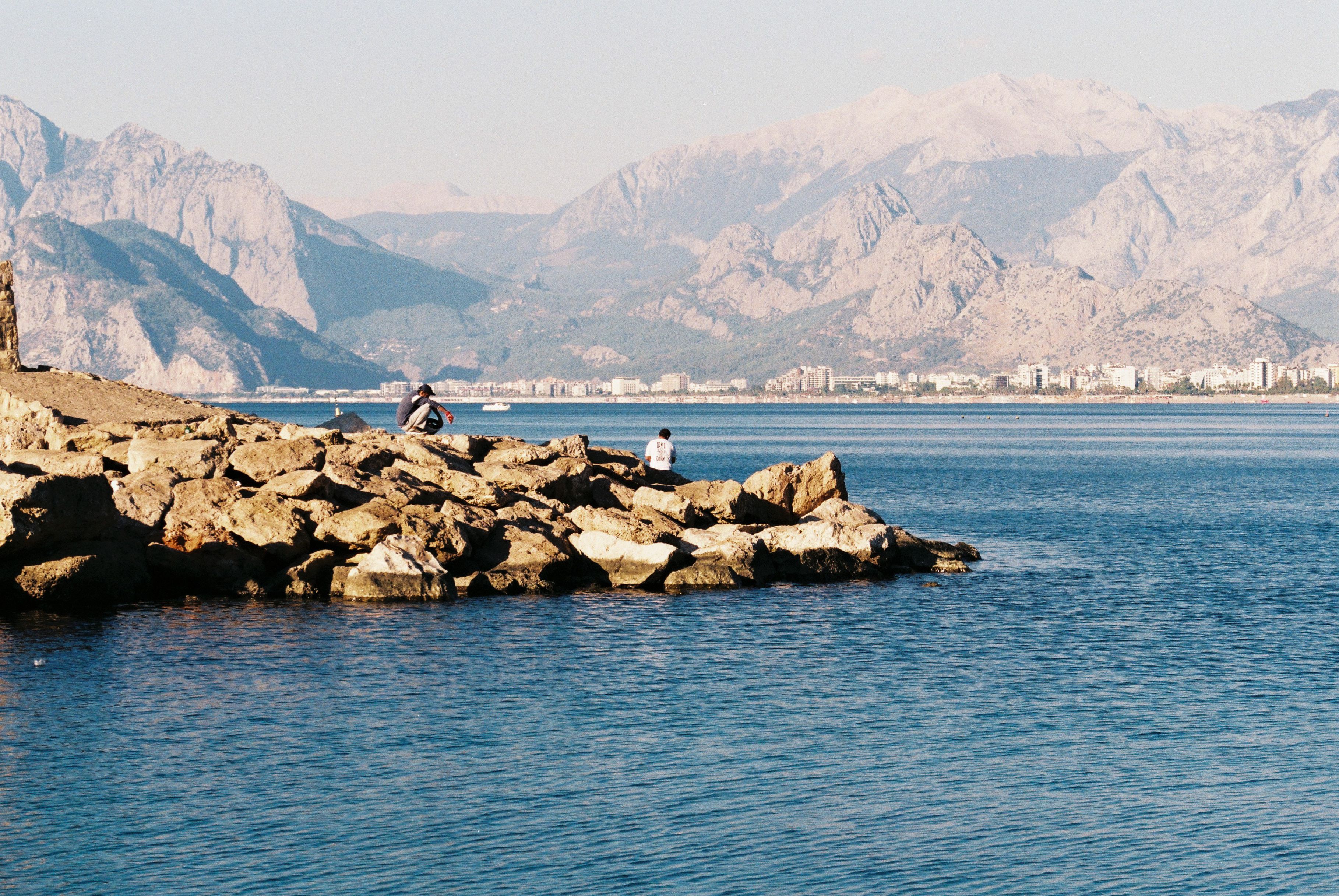 Photo of a Coast with Men Sitting on Rocks · Free Stock Photo