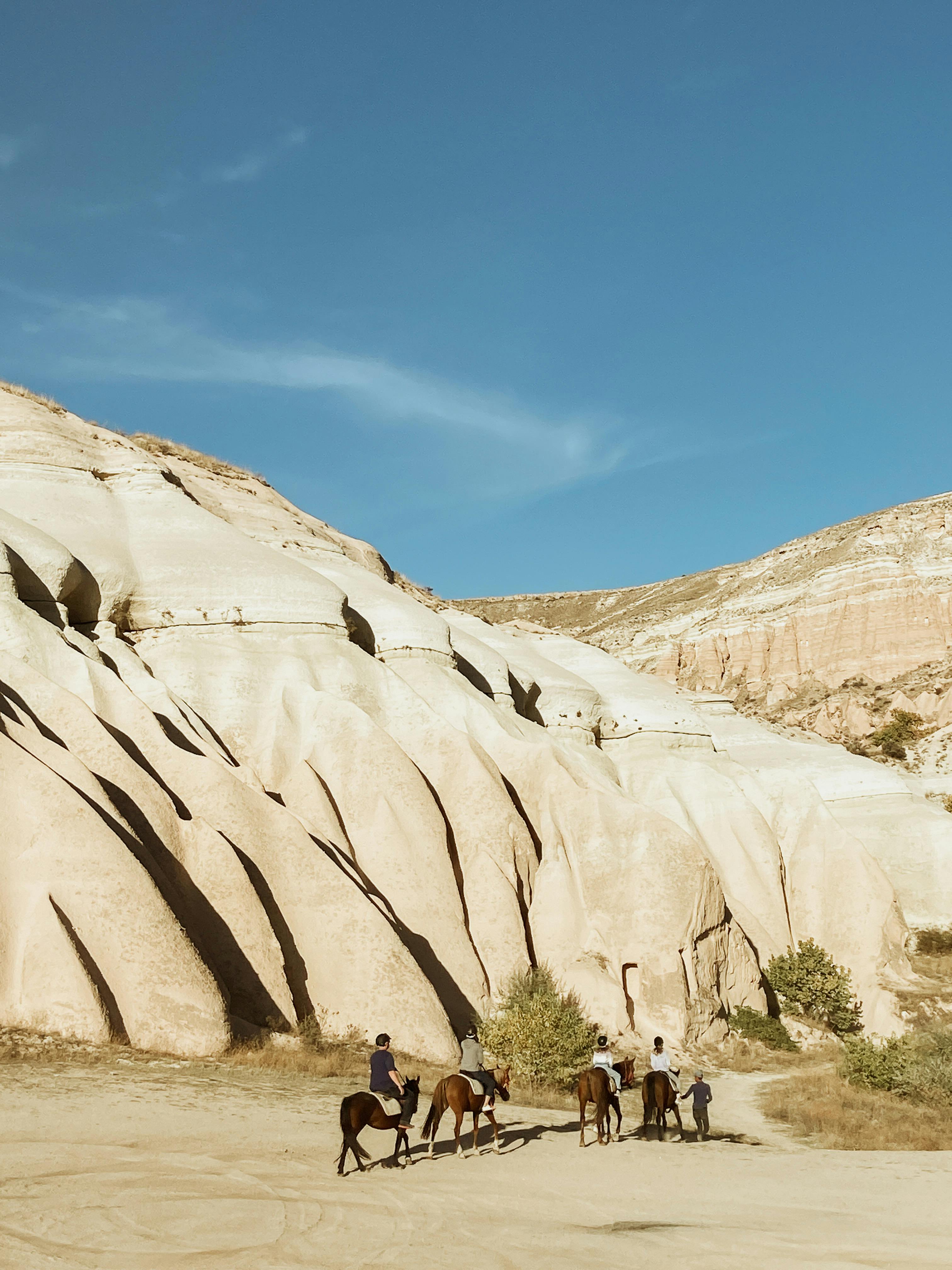 A Group of People Riding Horses Near a Rock Mountain Under Blue Sky ...