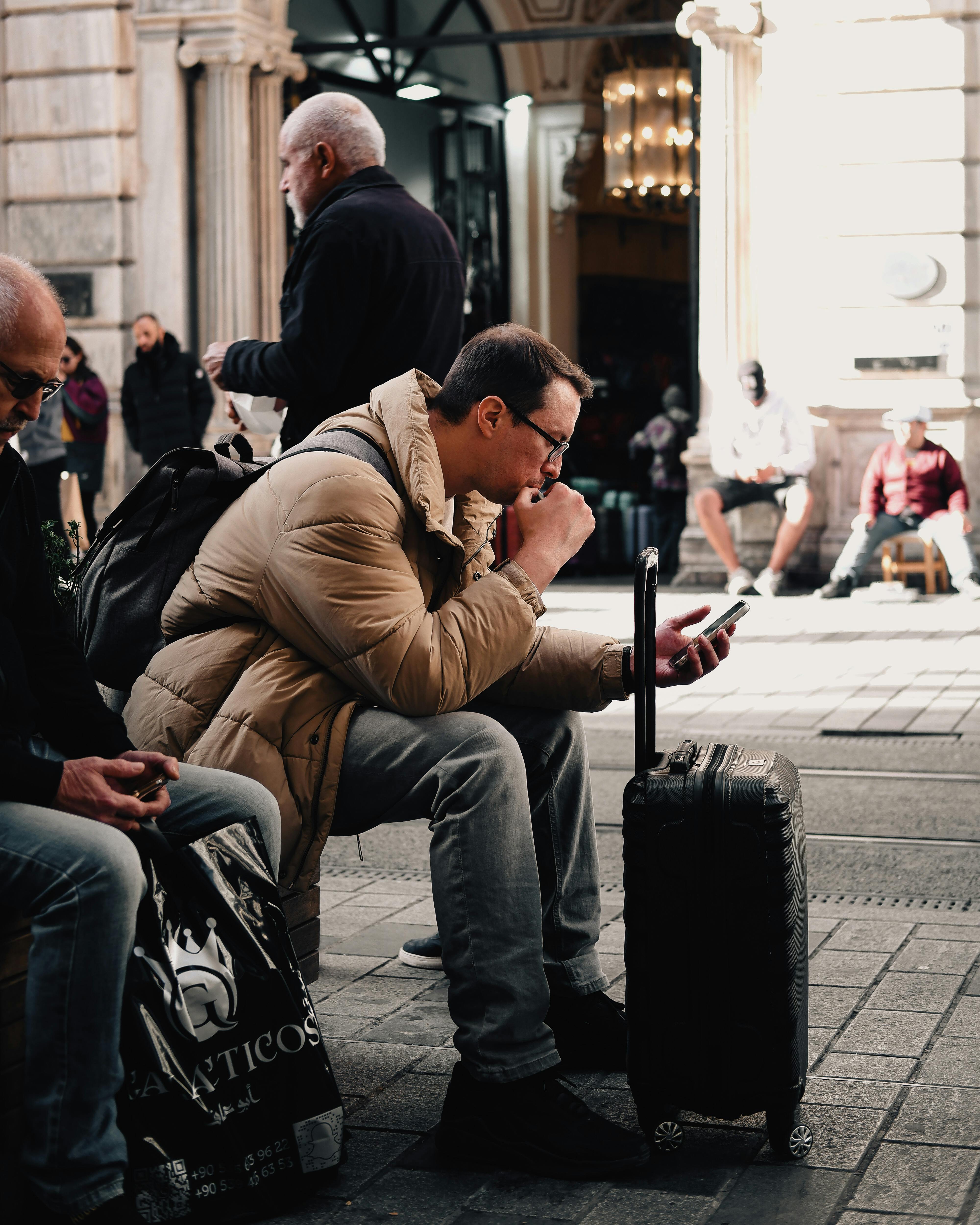 Man with Suitcase Sitting on Bench Using Phone · Free Stock Photo