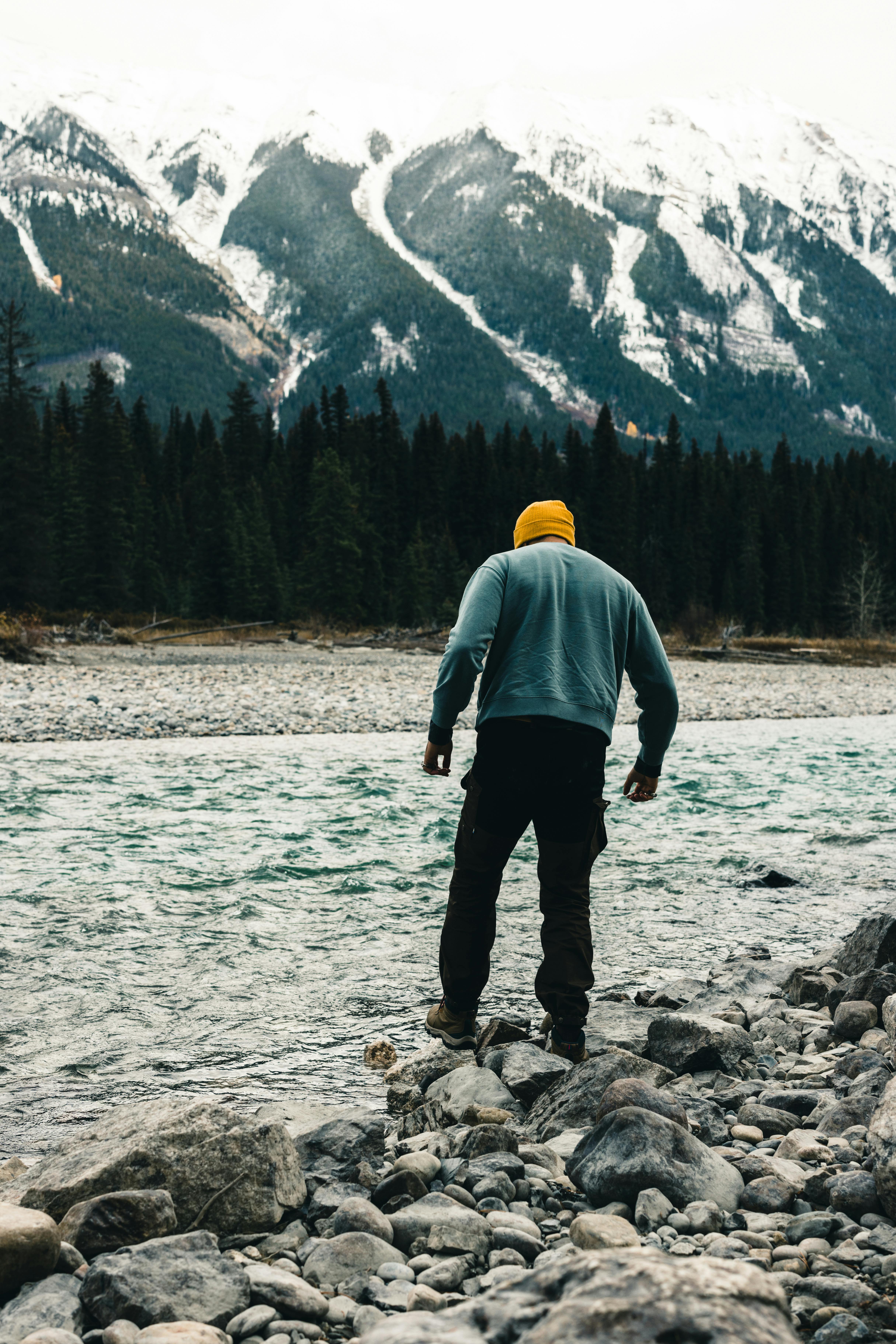 Man Standing on the Rocks near a Body of Water in a Valley with View of ...