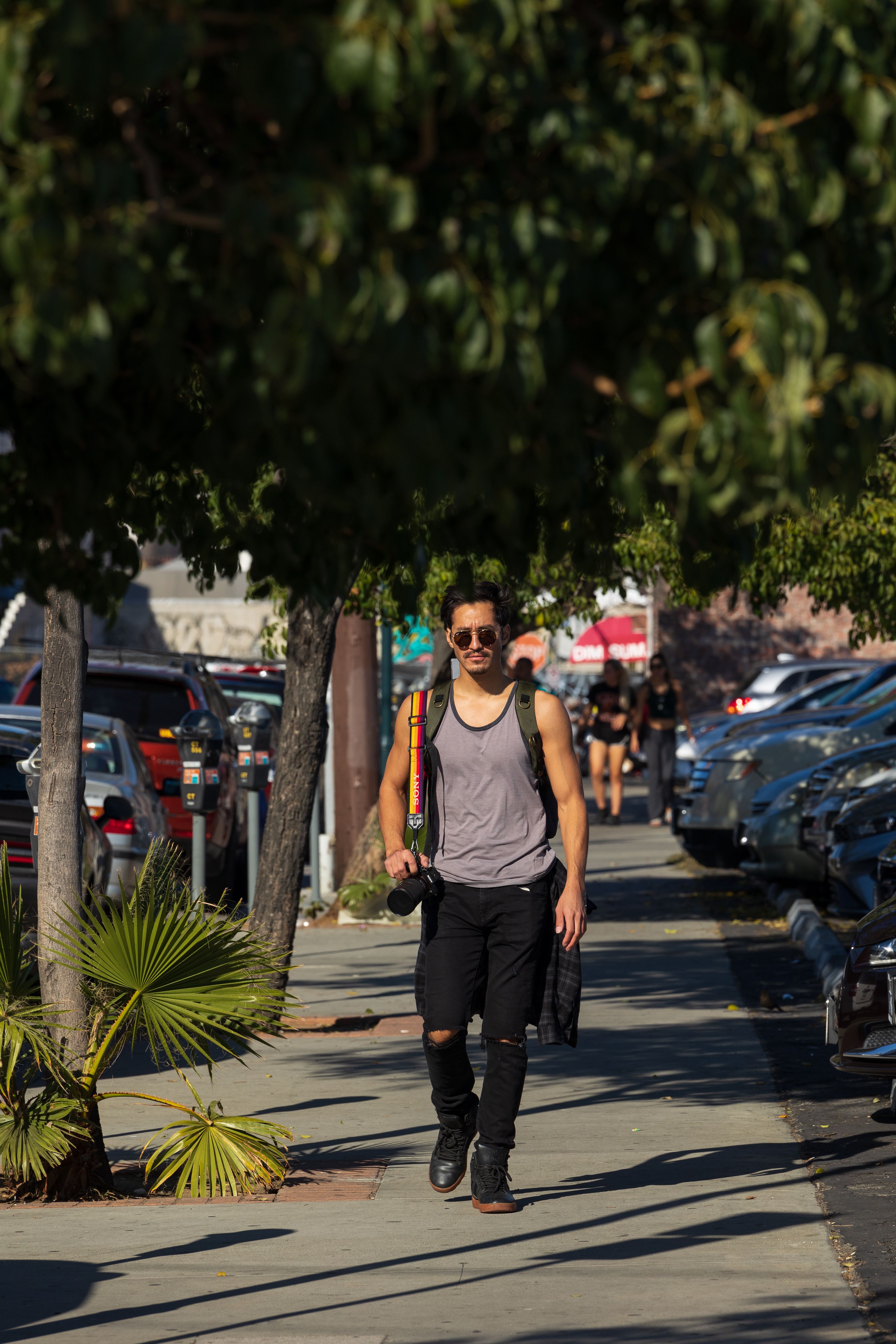 A Photographer Walking on the Sidewalk Holding a Camera · Free Stock Photo