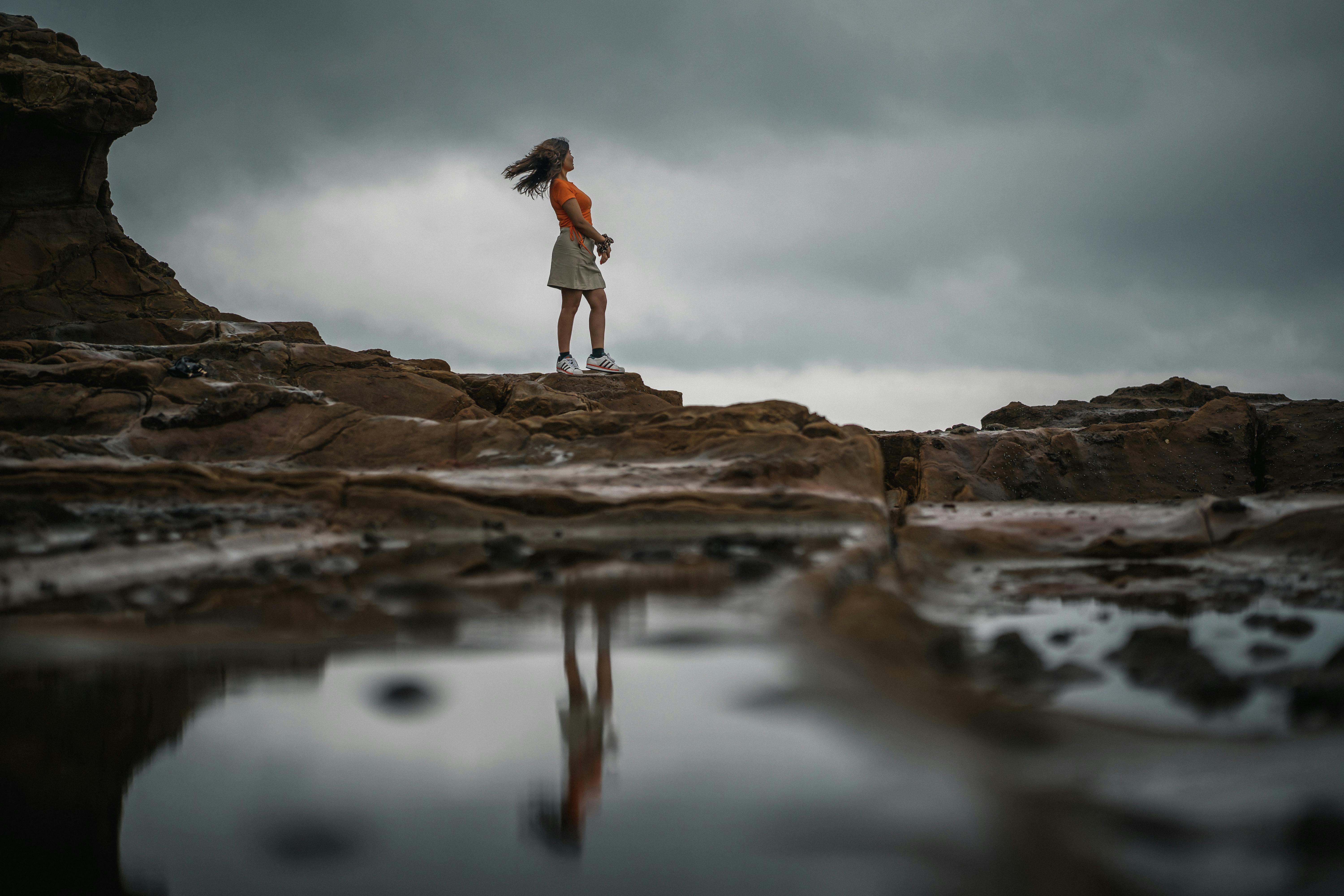 Woman Standing on Rock Formation on Windy Day · Free Stock Photo