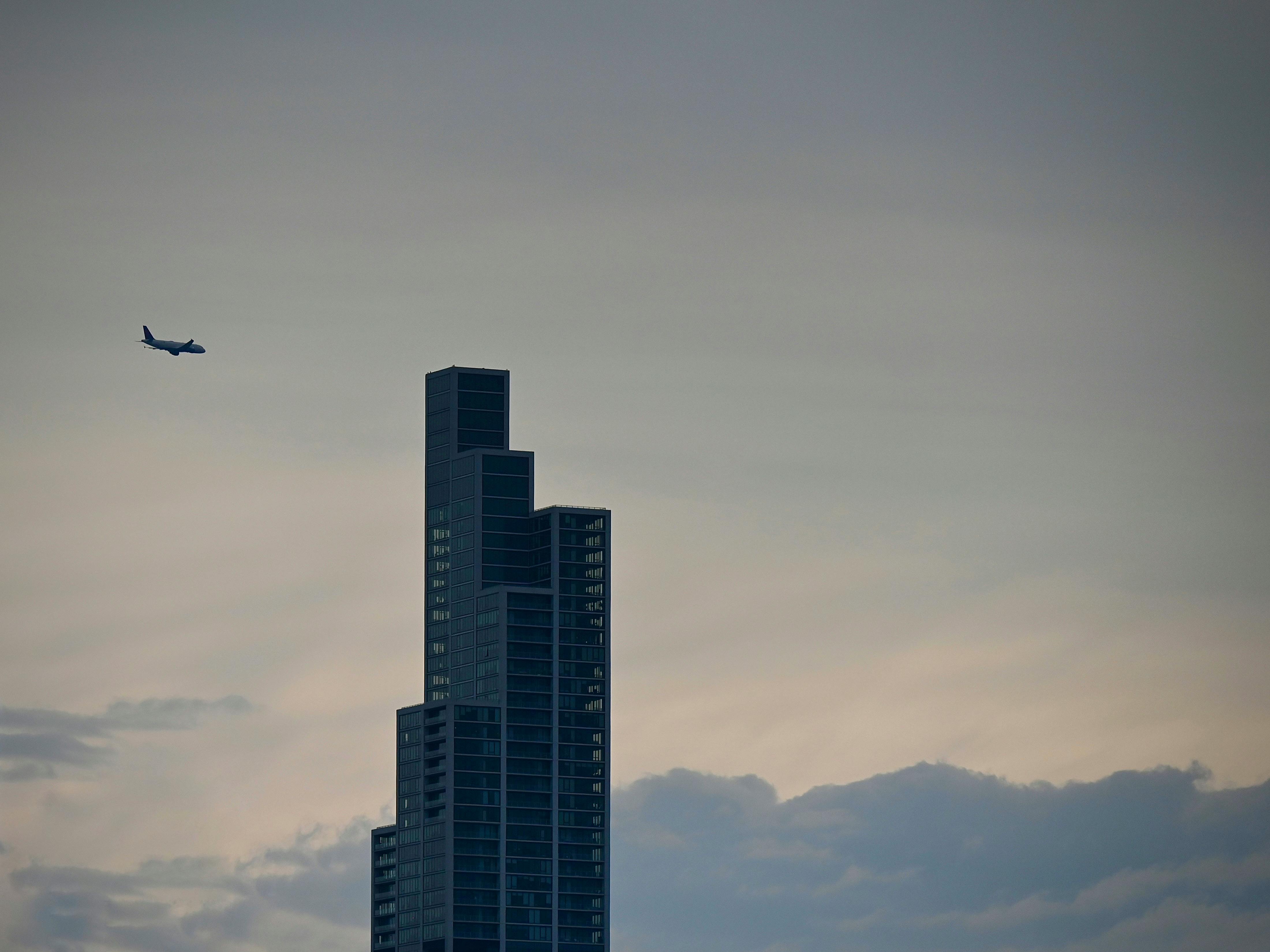 A High Rise Building Near a Flying Airplane Under Gray Skies · Free ...