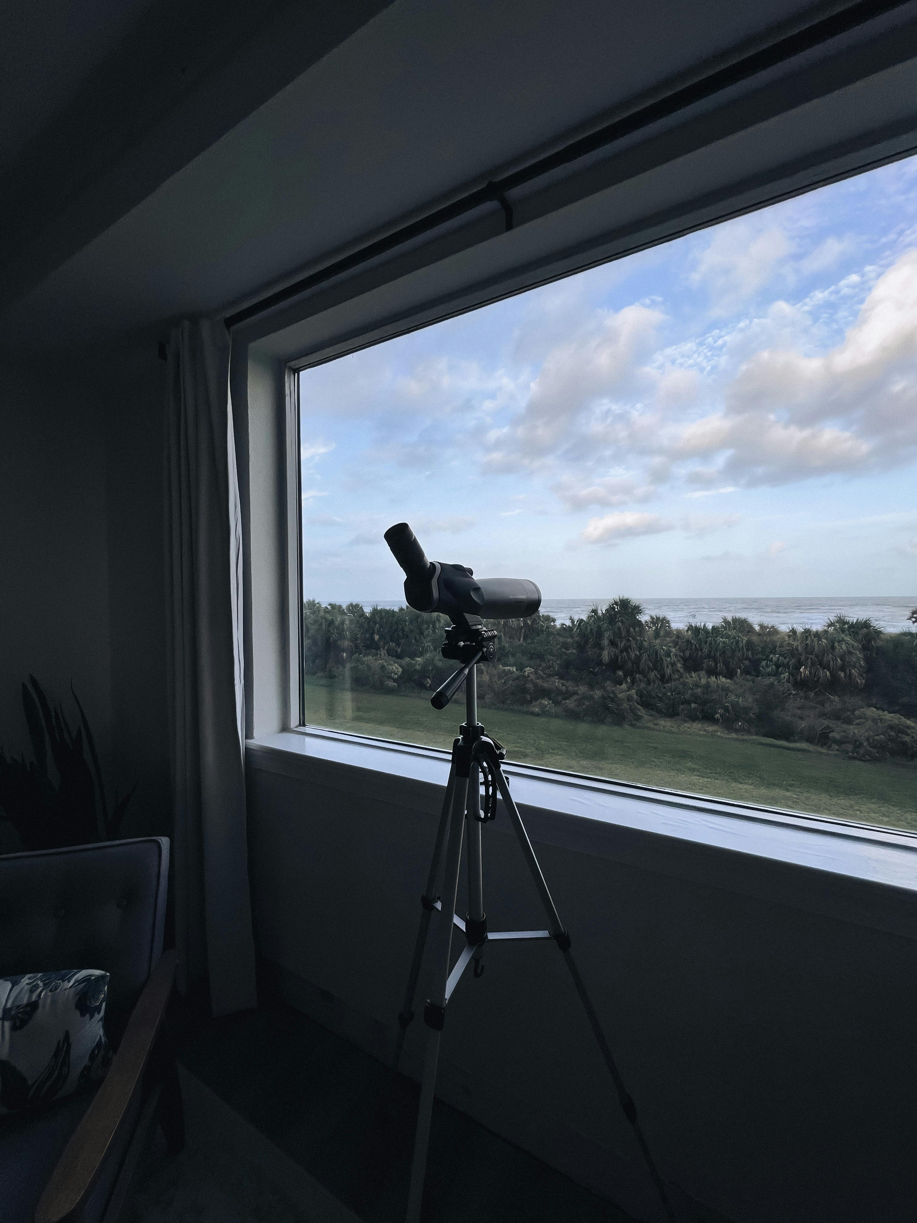 A Black Telescope in a Tripod Near a Glass Window · Free Stock Photo