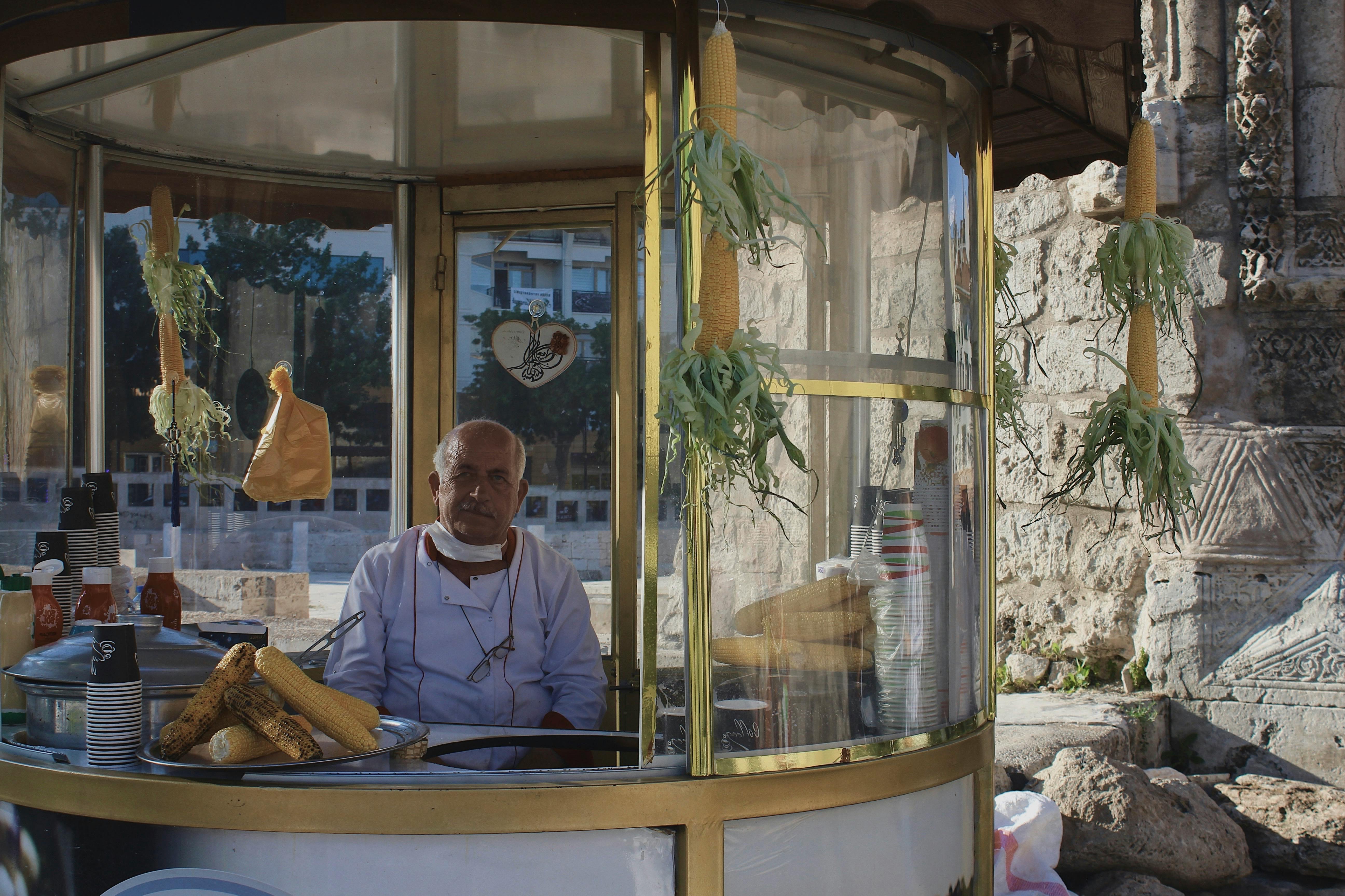 A Man in White Long Sleeve Shirt Sitting in a Corn Booth · Free Stock Photo