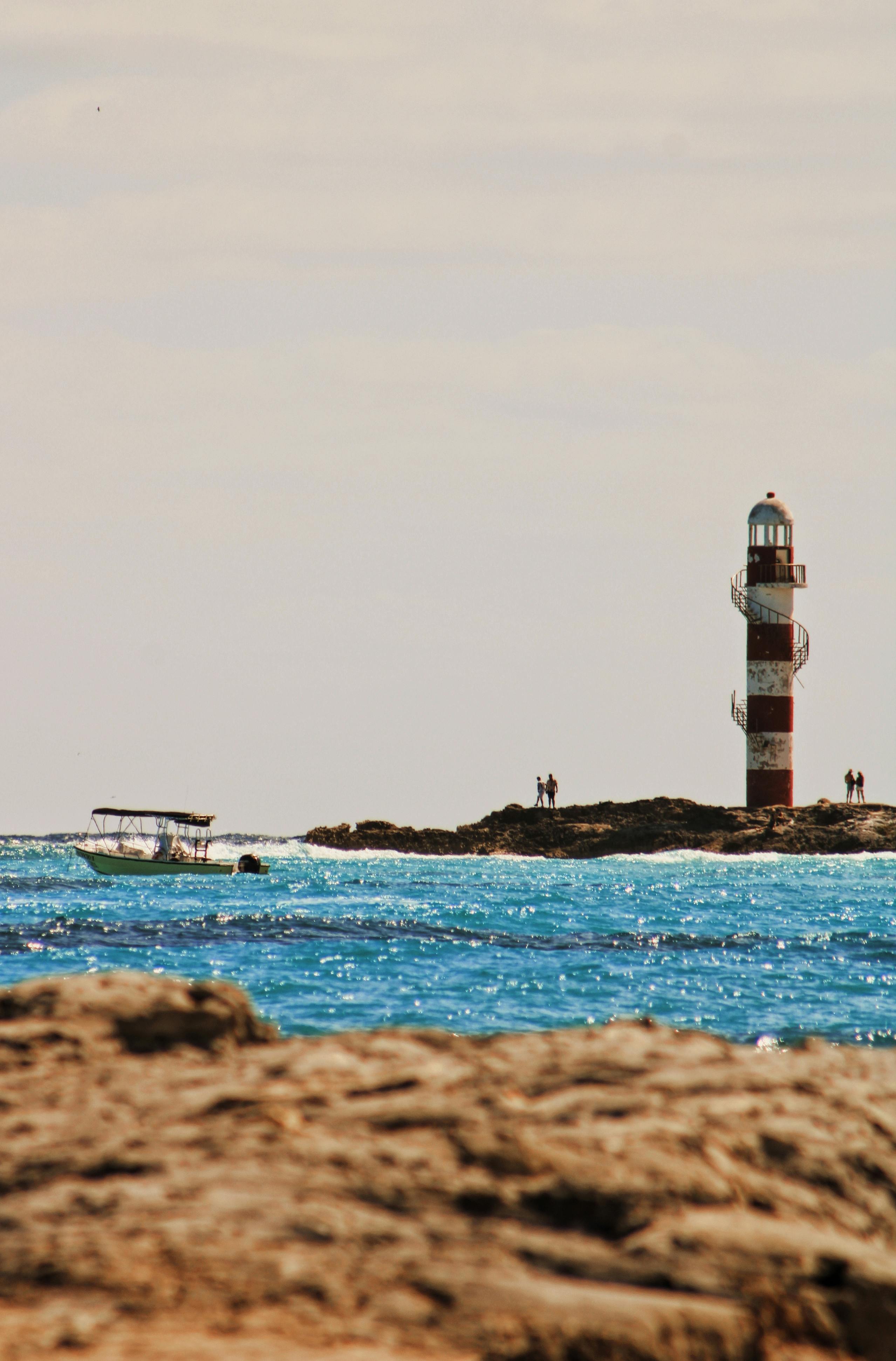White and Red Lighthouse on Brown Rock Formation Near Body of Water ...